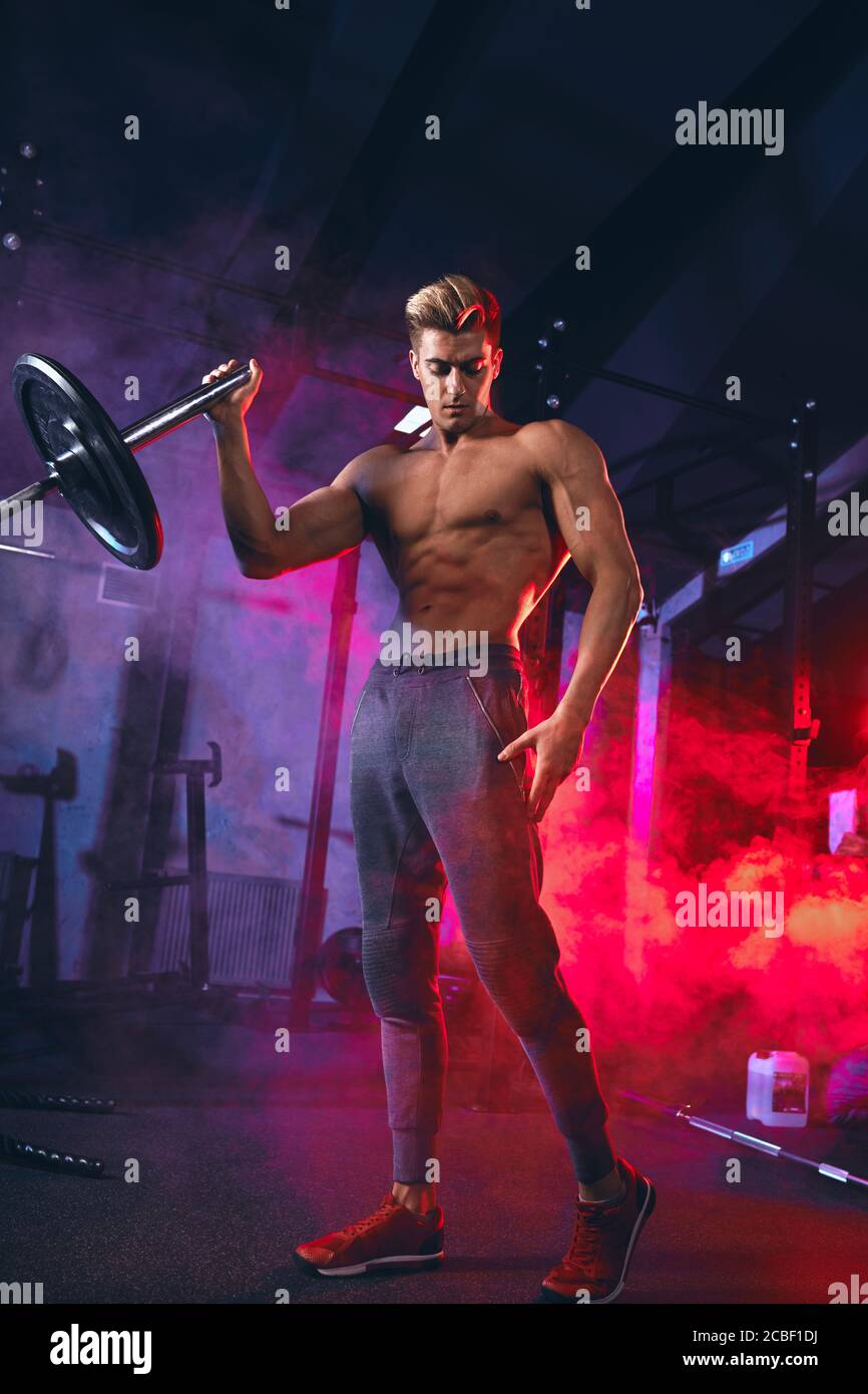 Ripped male personal trainer uploading weight plate on barbell before ...