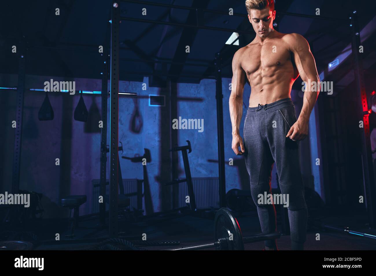 Ripped male personal trainer uploading weight plate on barbell before ...