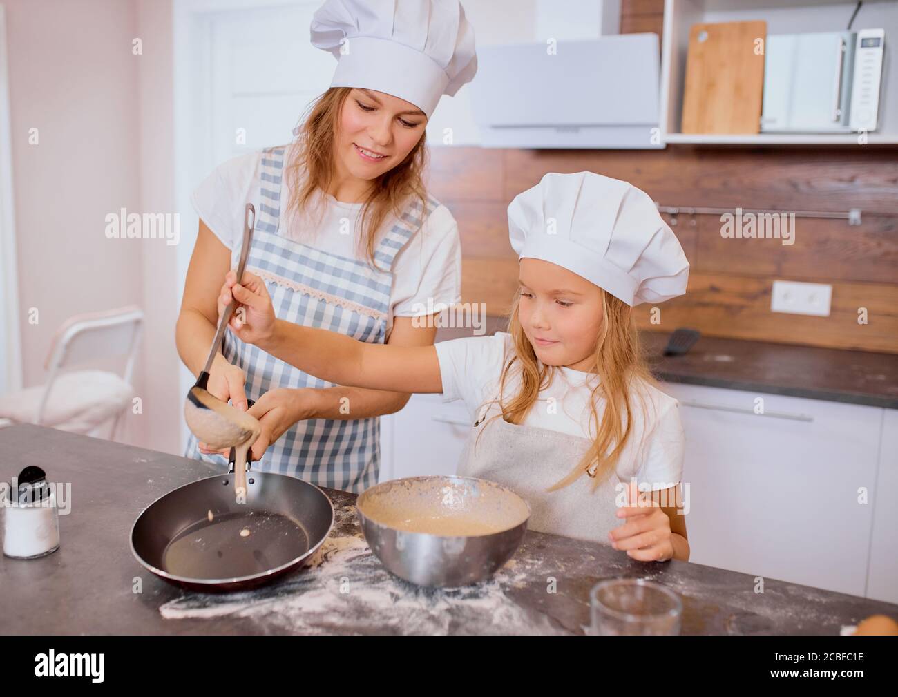 caucasian woman and child girl together in kitchen, woman teach kid ...
