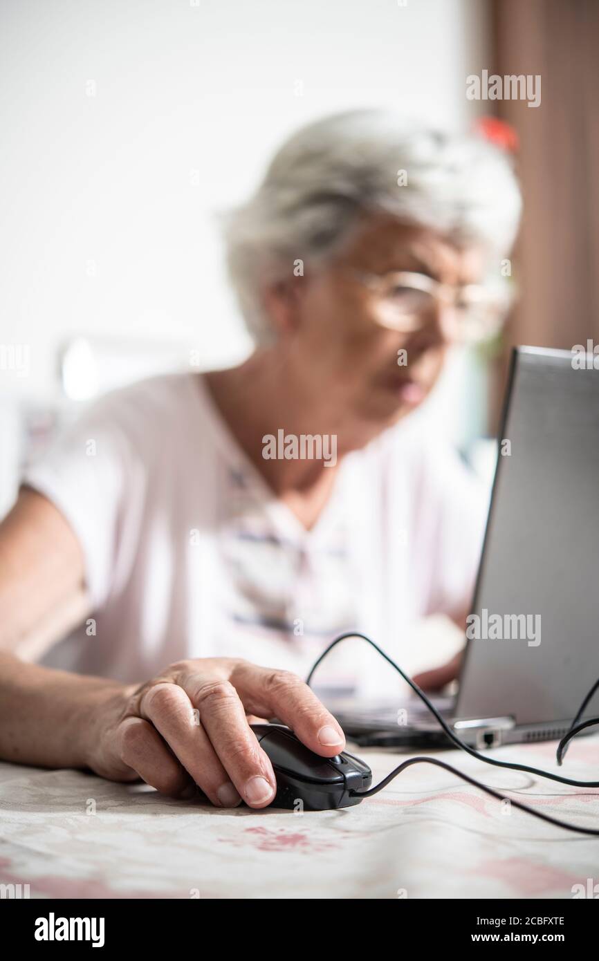 An elder lady with glasses staring at laptop's monitor while clicking ...