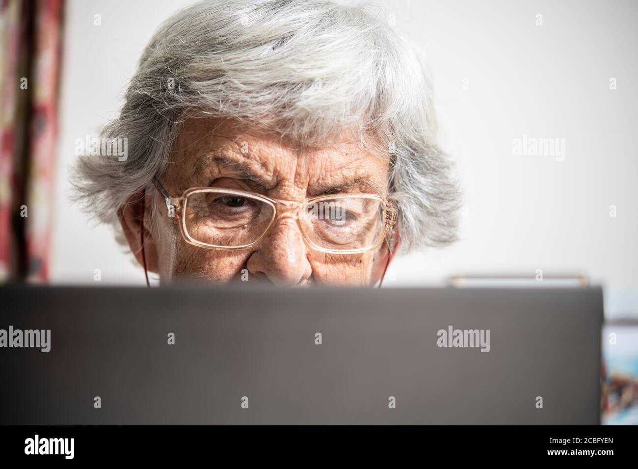 An elder lady with glasses staring at laptop's monitor while clicking ...