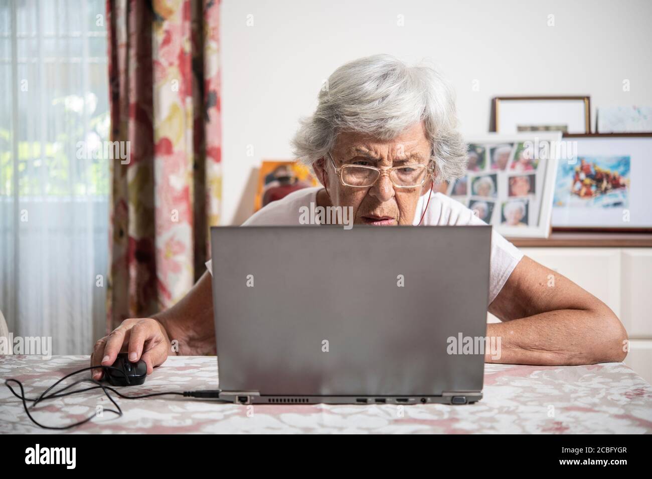 An elder lady with glasses staring at laptop's monitor while clicking ...
