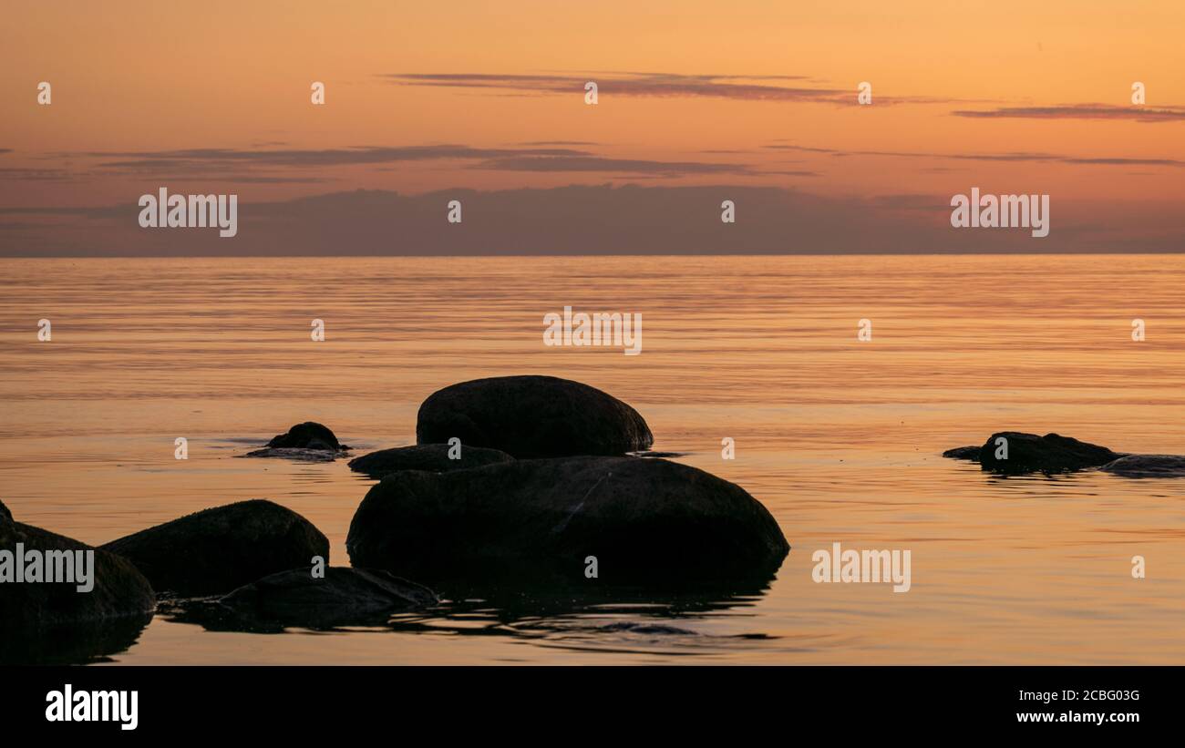 orange sunset by the sea, black stone silhouettes against the sea ...