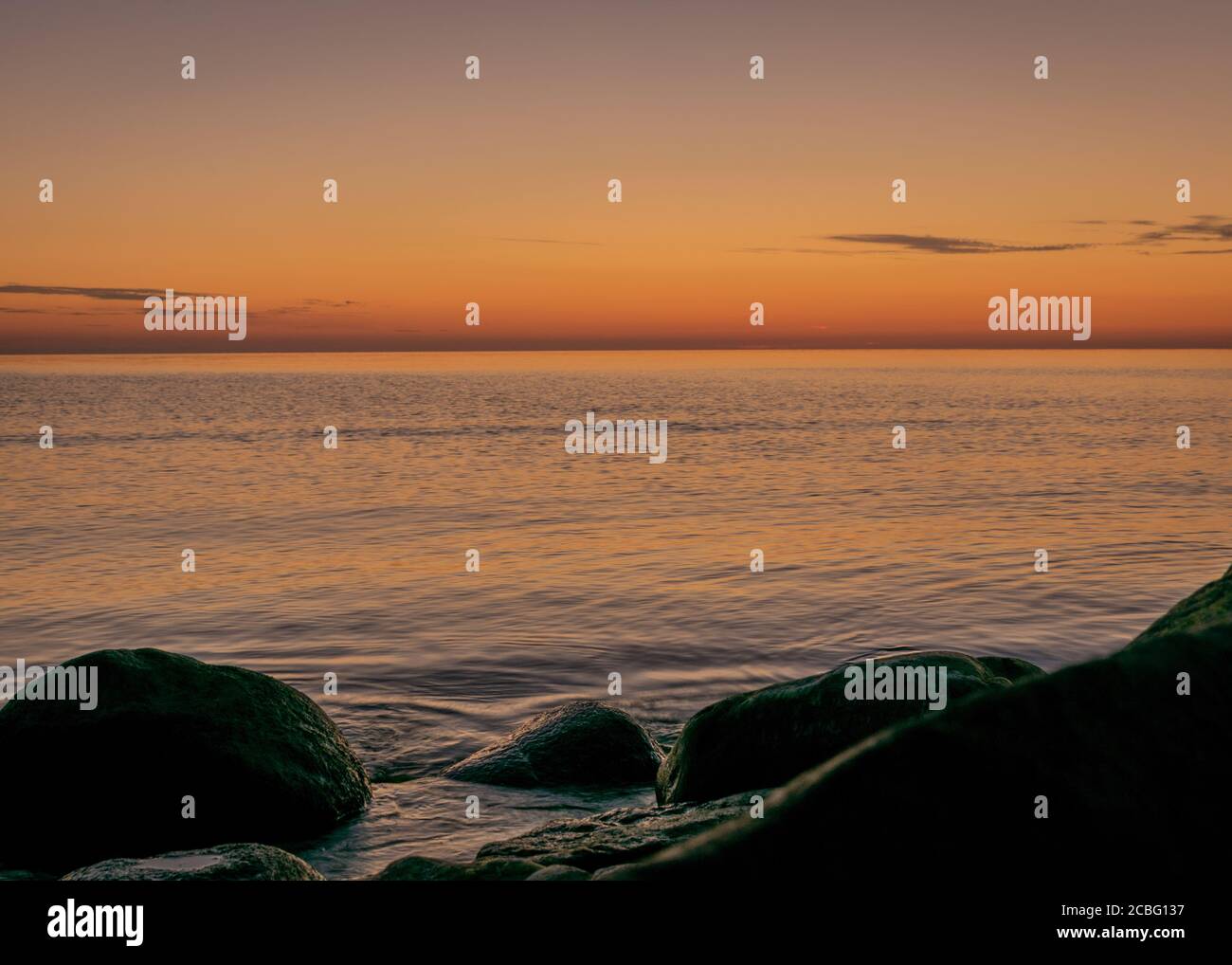 orange sunset by the sea, black stone silhouettes against the sea ...