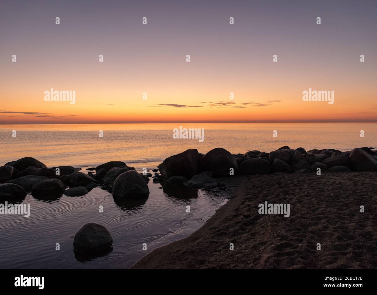 orange sunset by the sea, black stone silhouettes against the sea ...