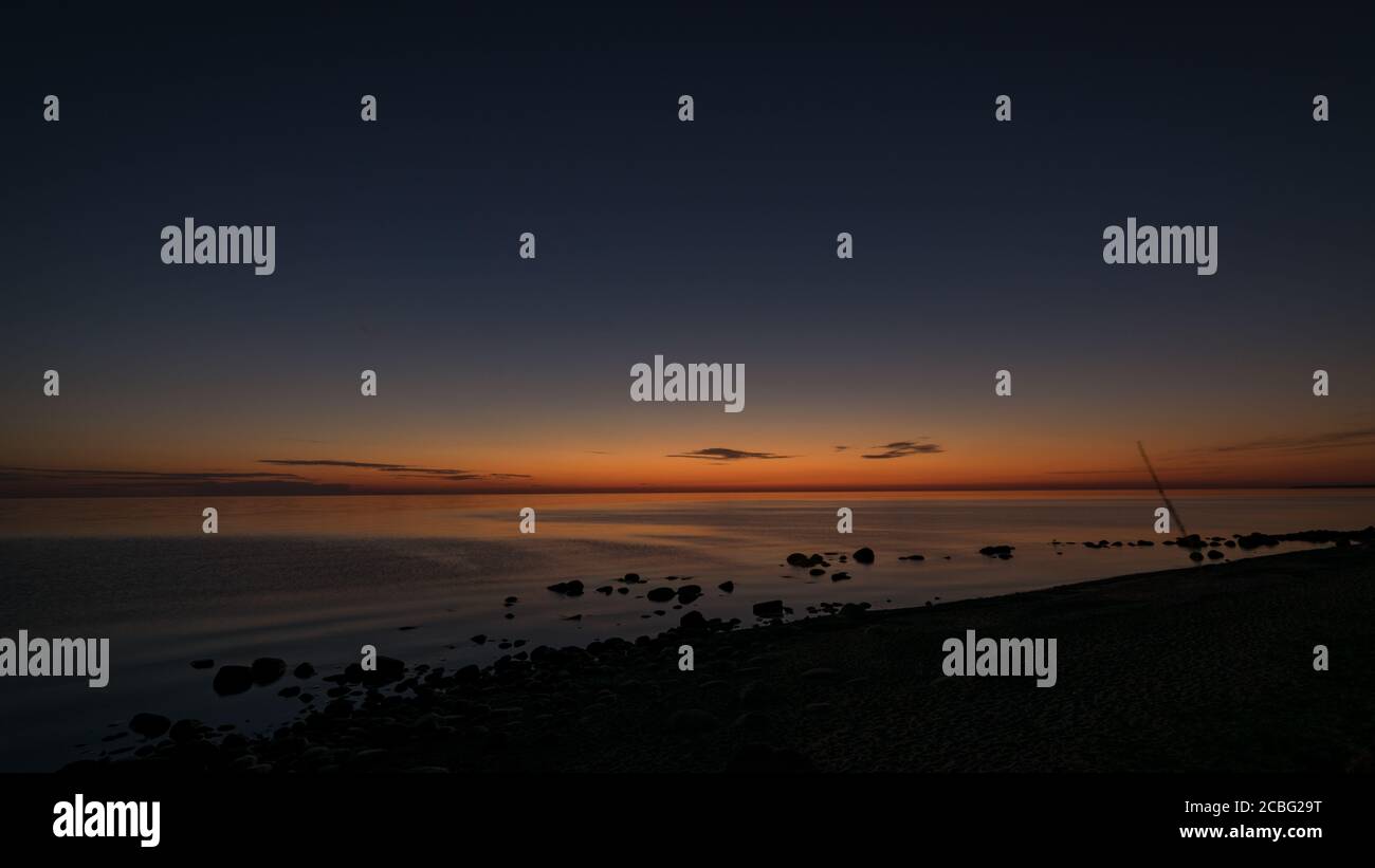 orange sunset by the sea, dark stone silhouettes in the foreground ...