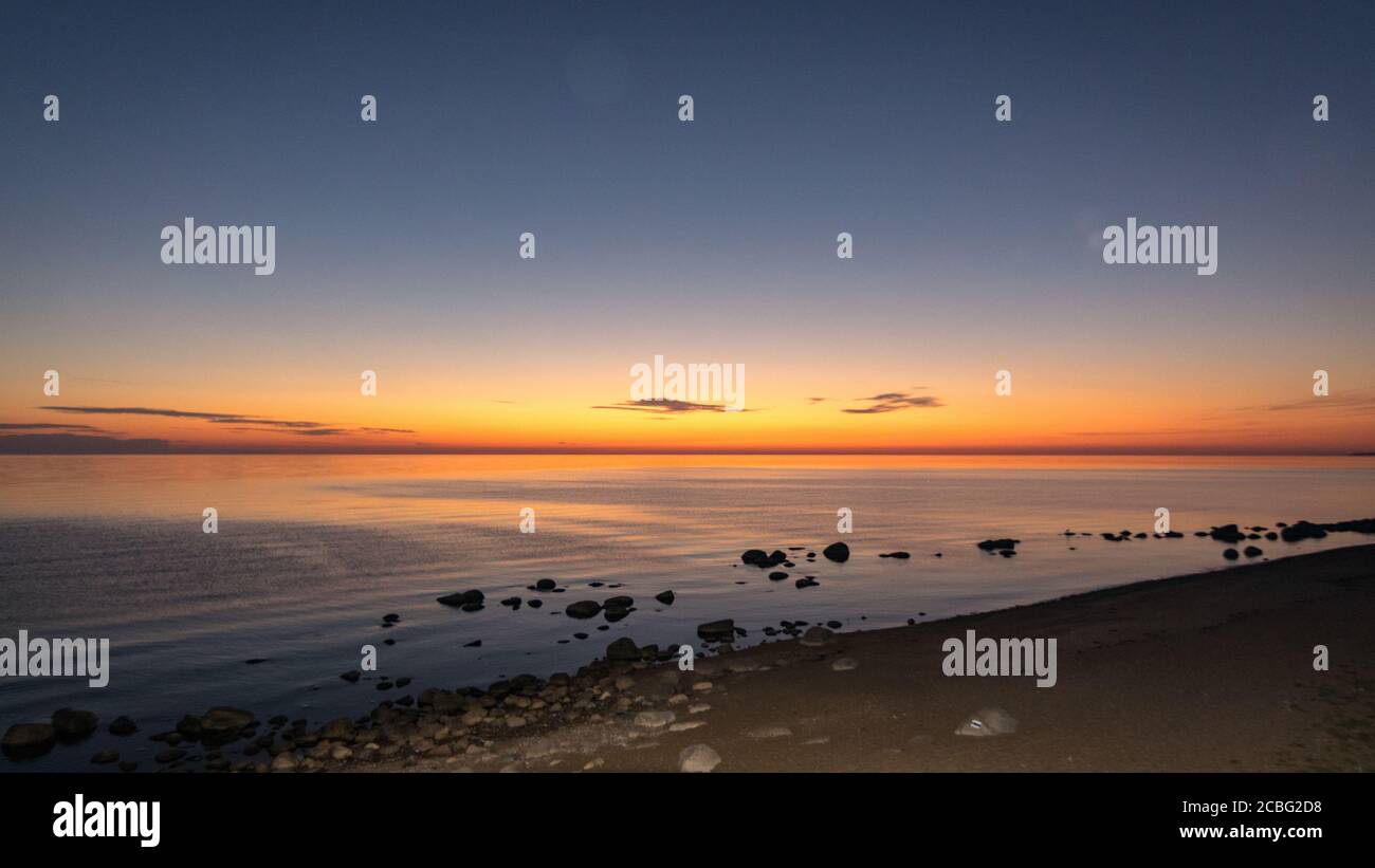 orange sunset by the sea, black stone silhouettes against the sea ...