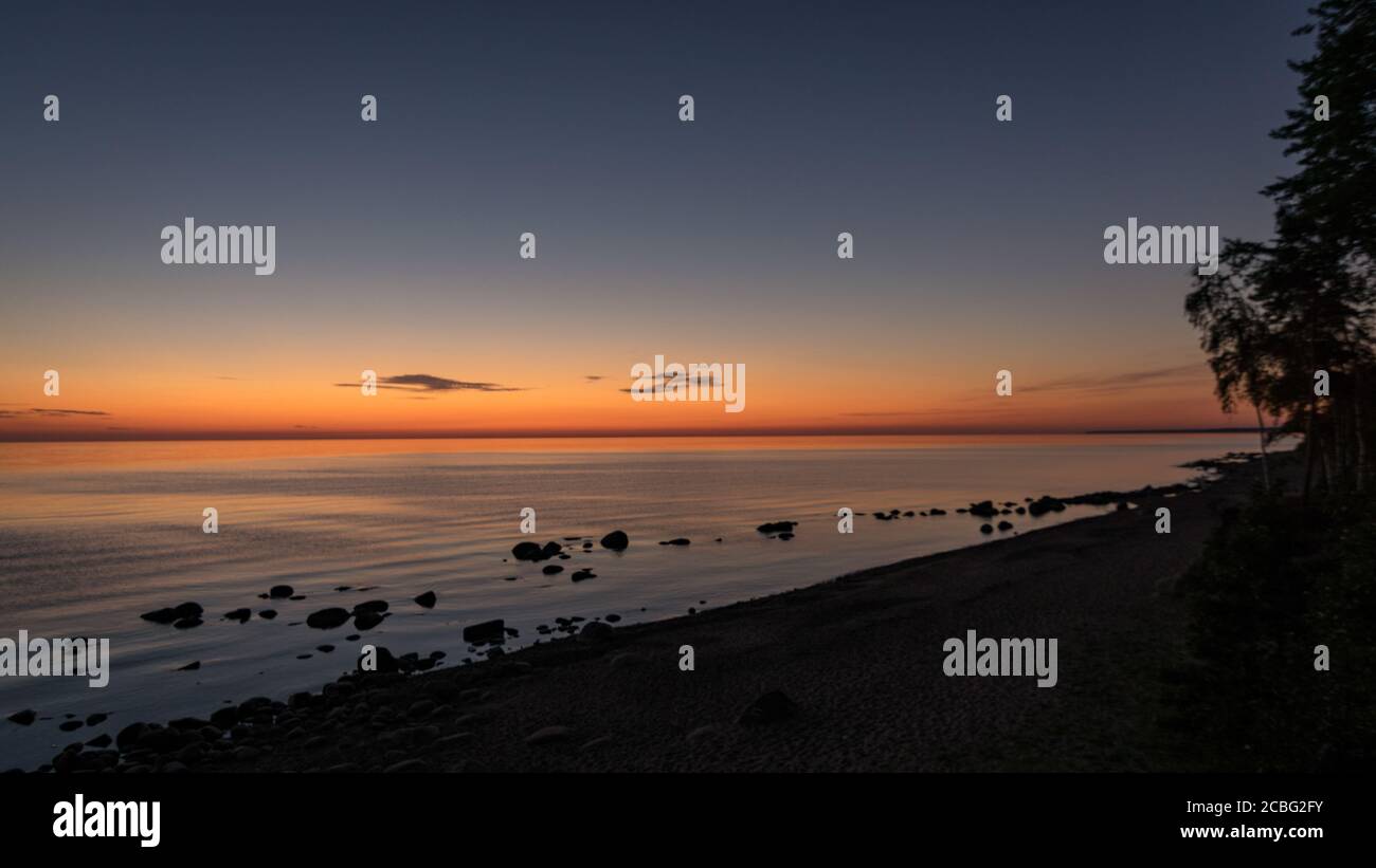 orange sunset by the sea, dark stone silhouettes in the foreground ...
