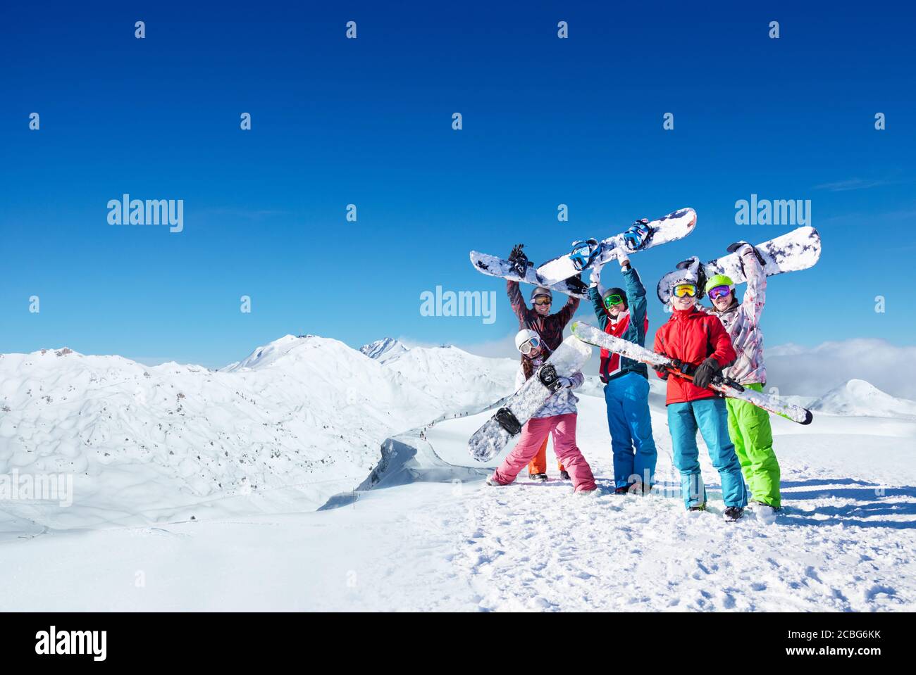 Large group of young snowboarders lift snowboards over head standing on ...