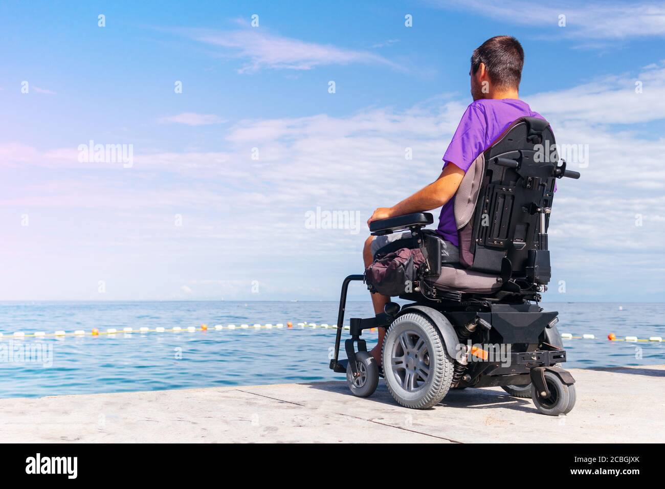 Man sitting in a wheelchair looking at sea. Head and spine injury ...
