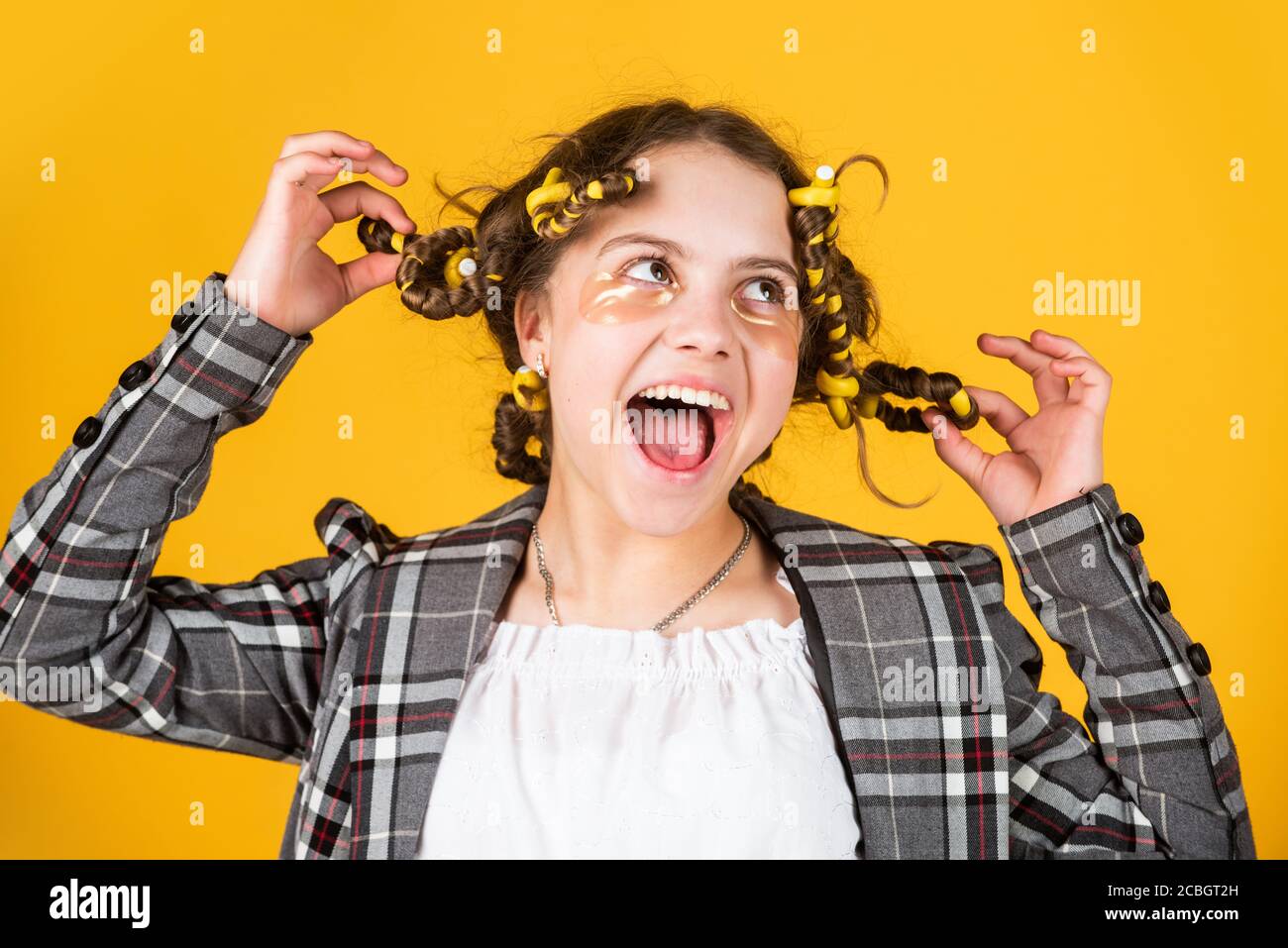 Girl with curlers and hair clips in her hair on yellow background ...