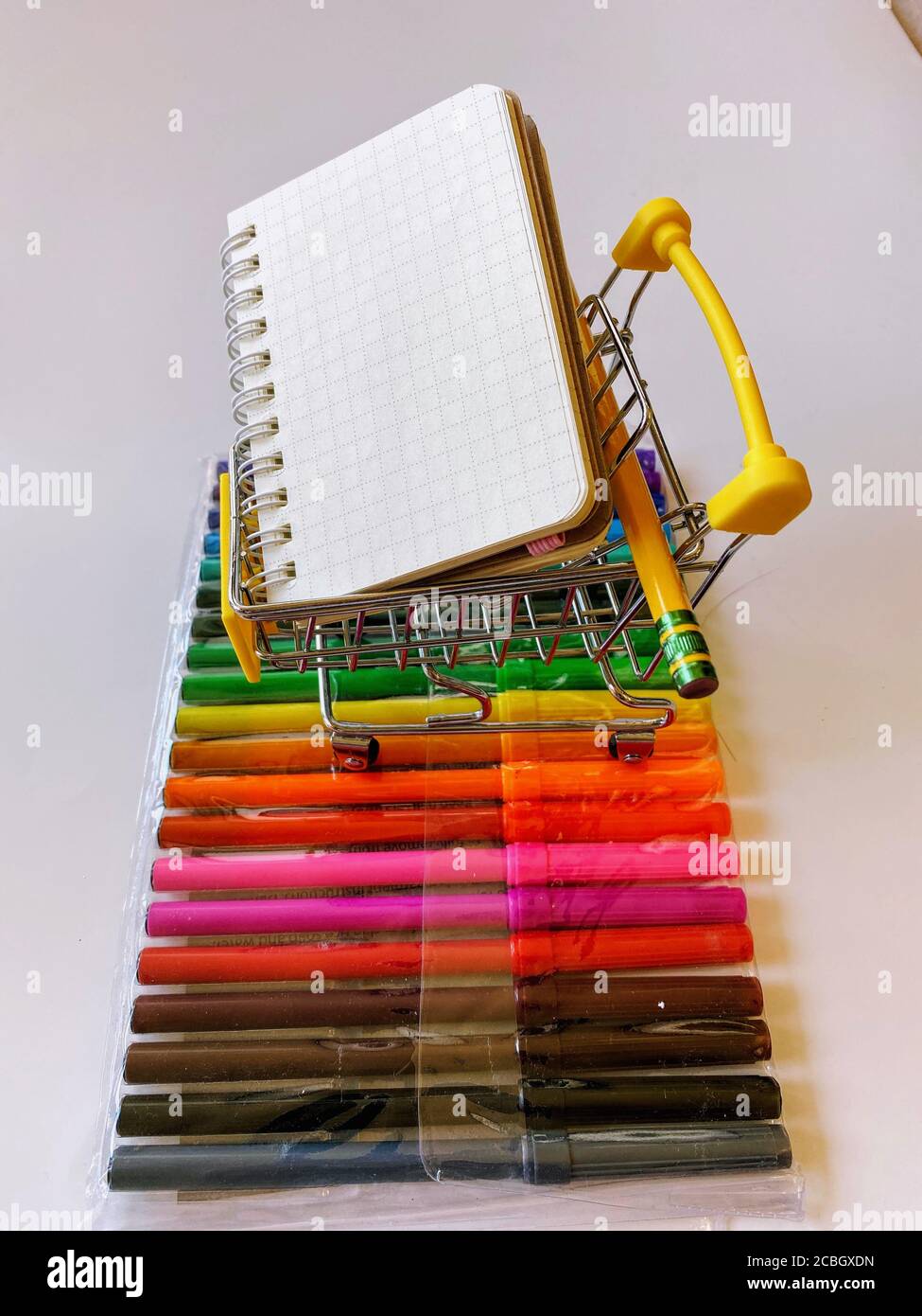 Miniature yellow shopping cart with notepad on colorful pens Stock ...