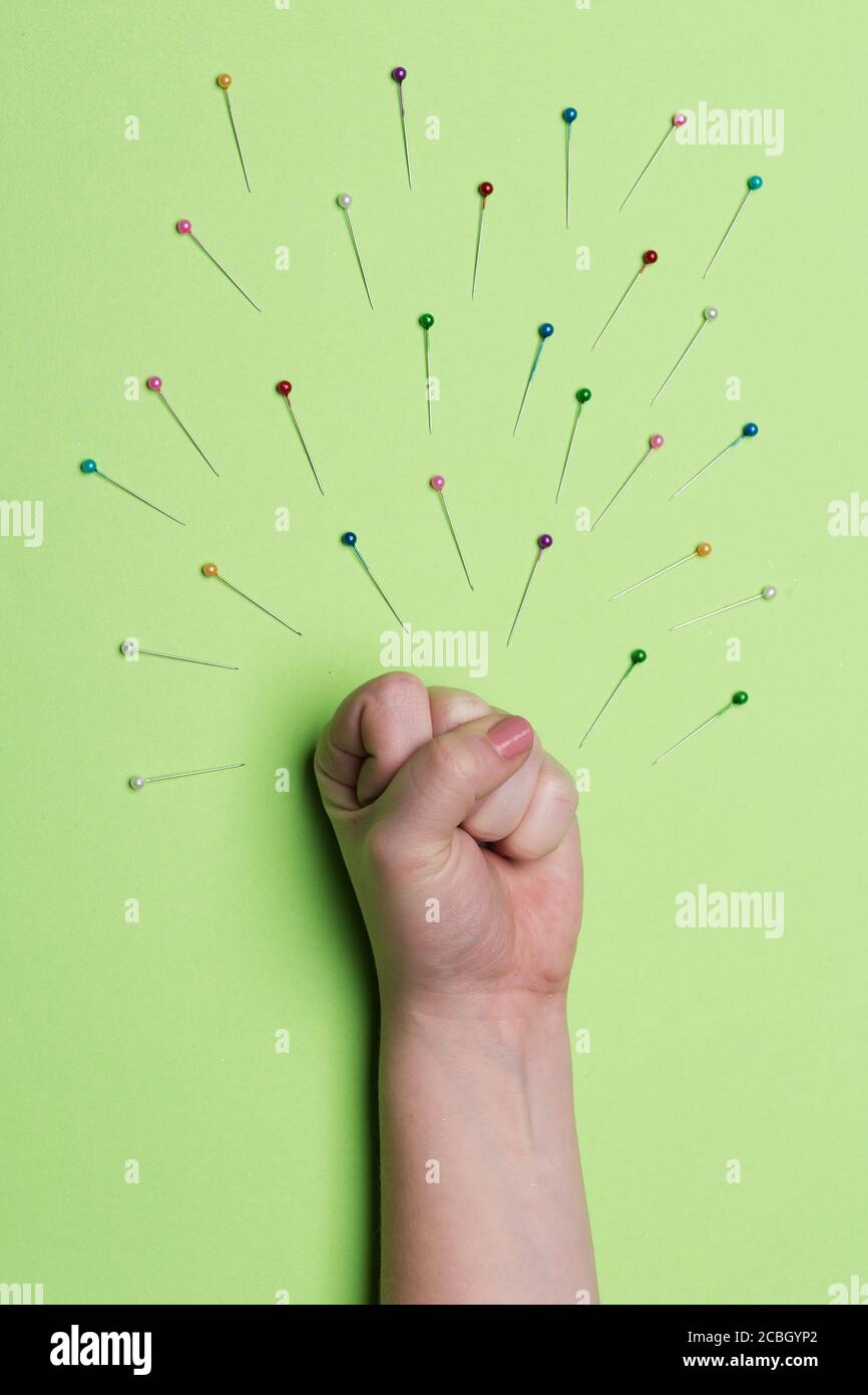 Fist placed near pins on light green background. Female hand as center ...