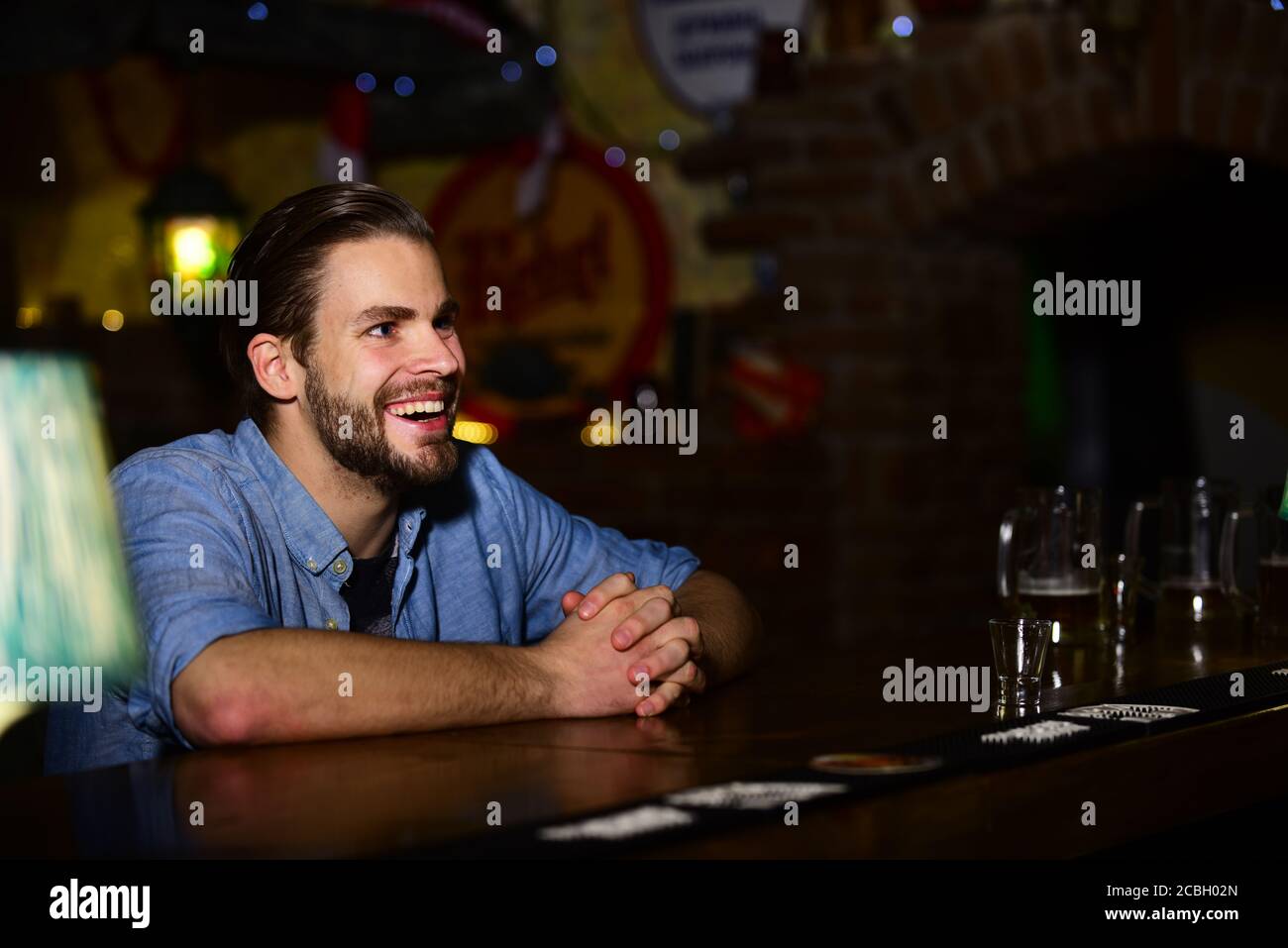 Man sits in bar near empty shot glass. Macho with beard sits in bar on ...