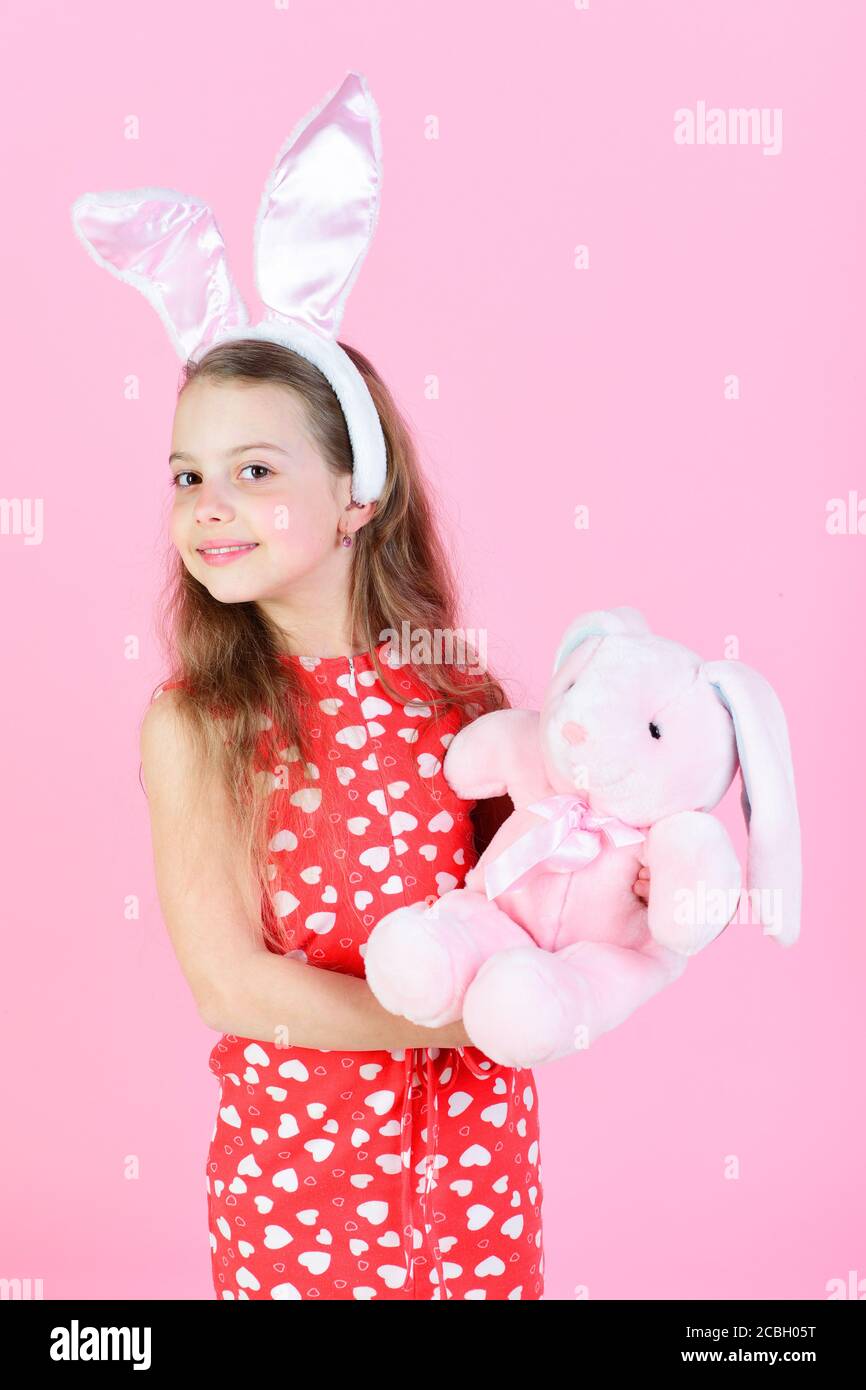 Happy girl holding rabbit toy on pink background. Child smiling with ...