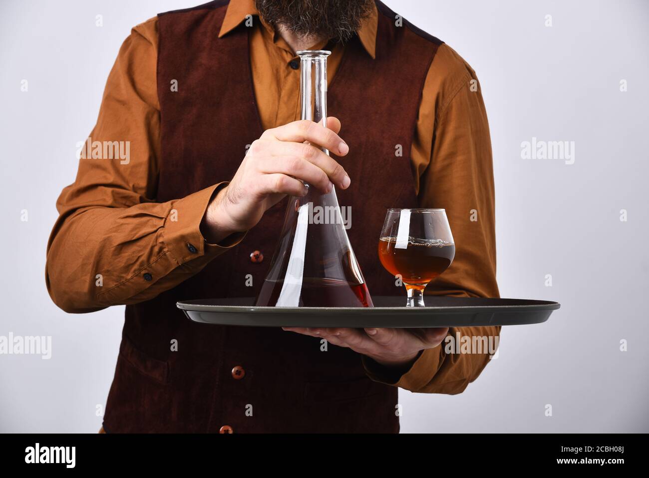 Waiter with glass and bottle of whiskey on tray. Bearded man holds ...