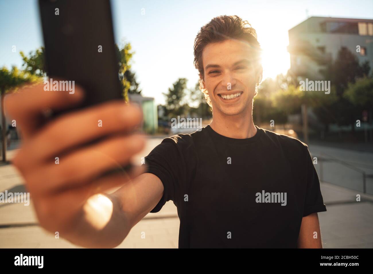 Smiling European man taking selfie through mobile phone in city on ...