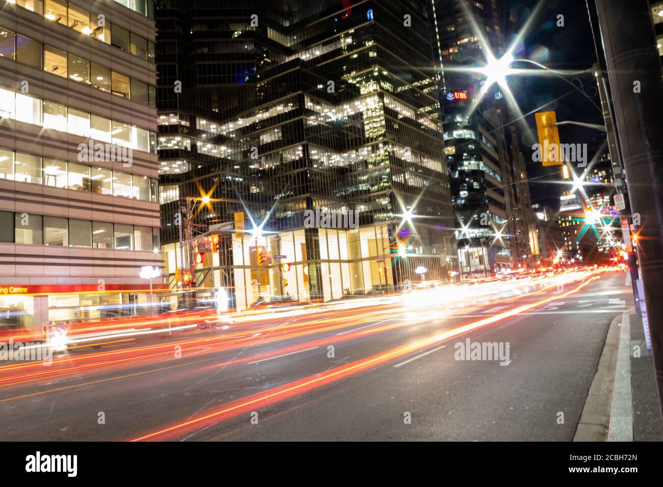 Car lights stream down a Toronto downtown city street in the evening ...