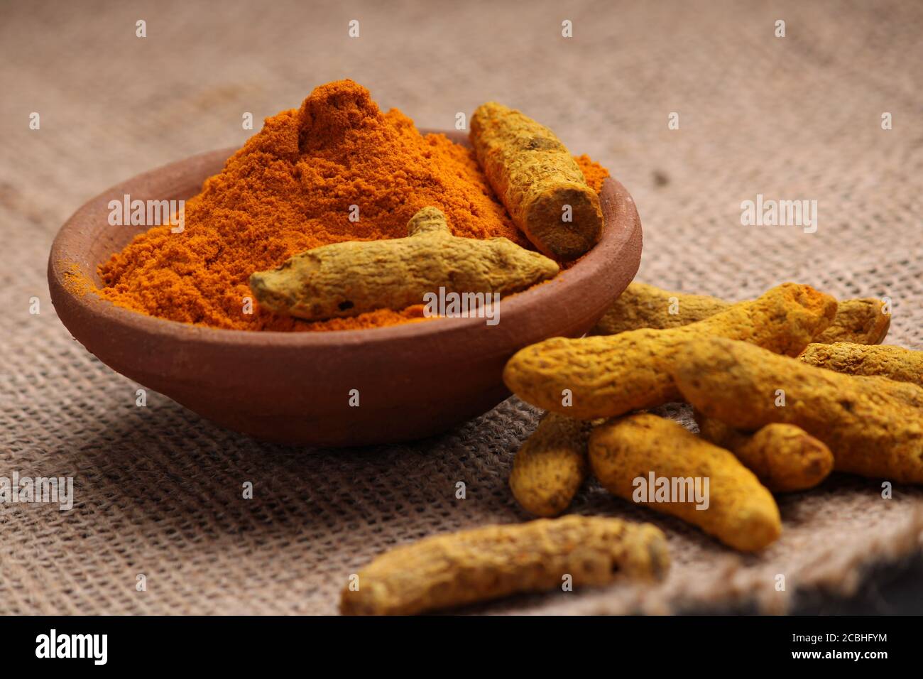 turmeric powder in earthen bowl with turmeric root on jute table cloth ...