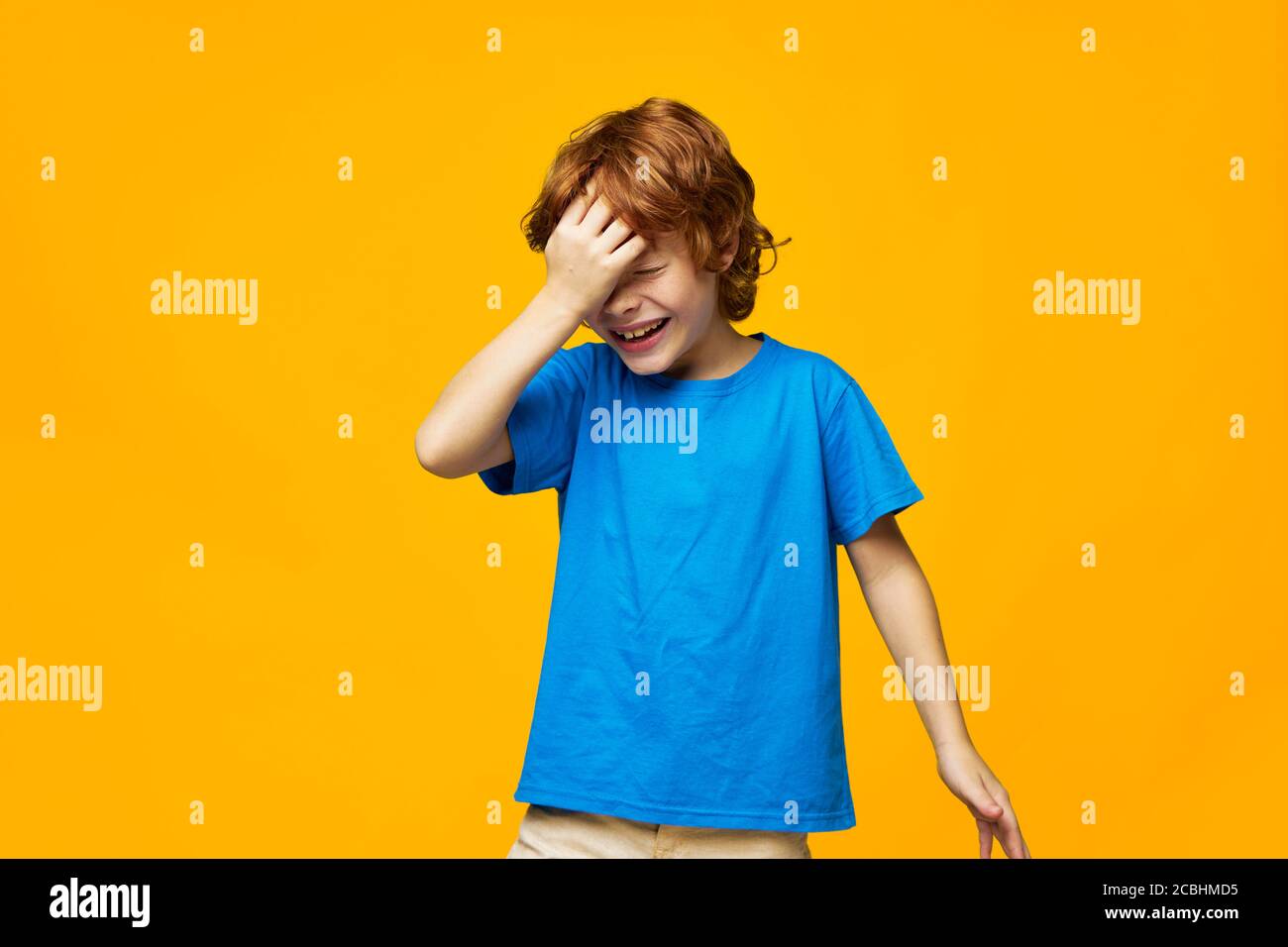 red-haired child frecklesA boy with red hair holds his hand on his face ...
