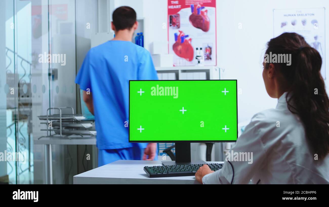 Physician using computer with chroma key and assistant holding patient ...