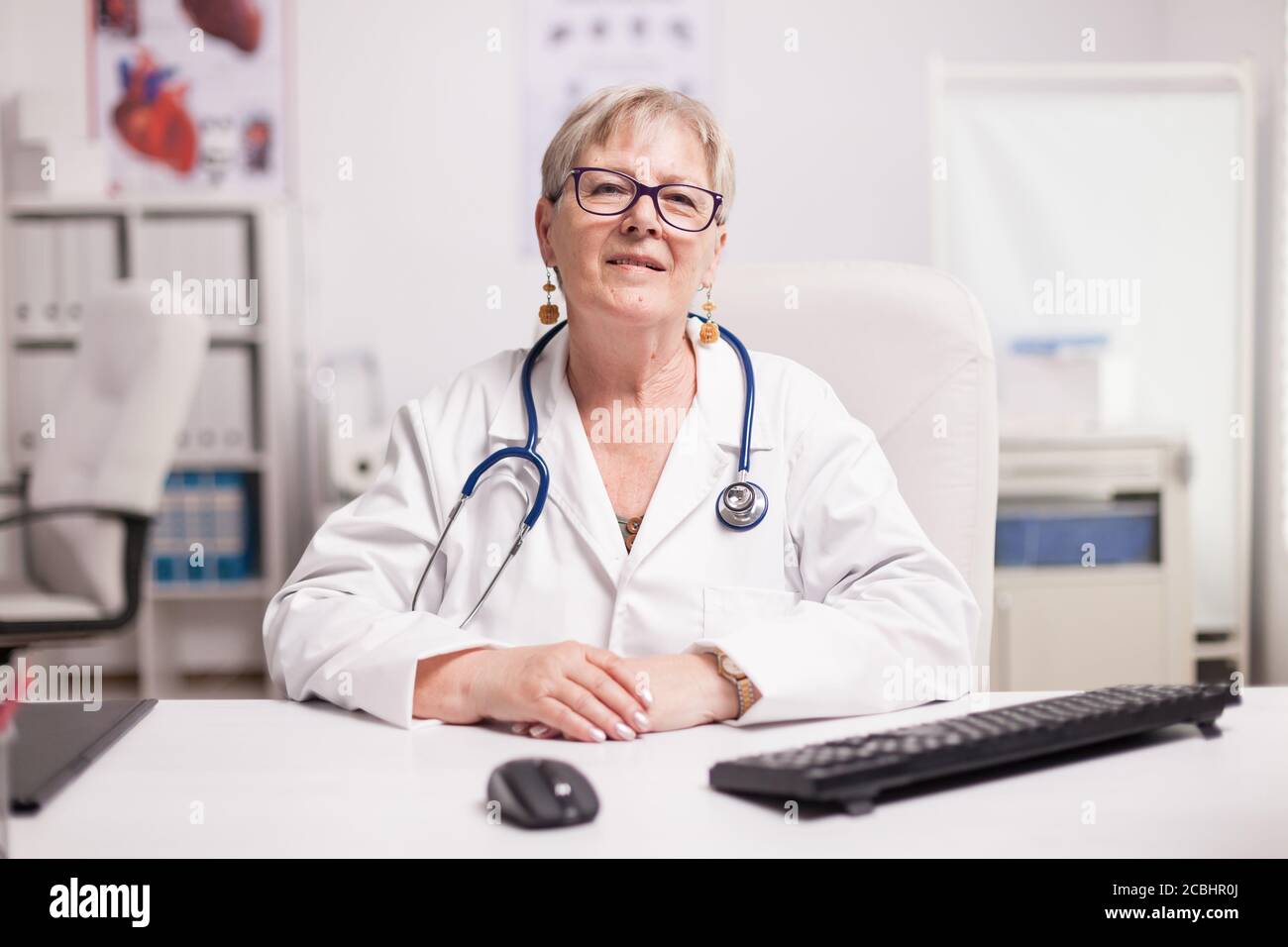Senior doctor with stethoscope wearing white coat smiling to camera in ...