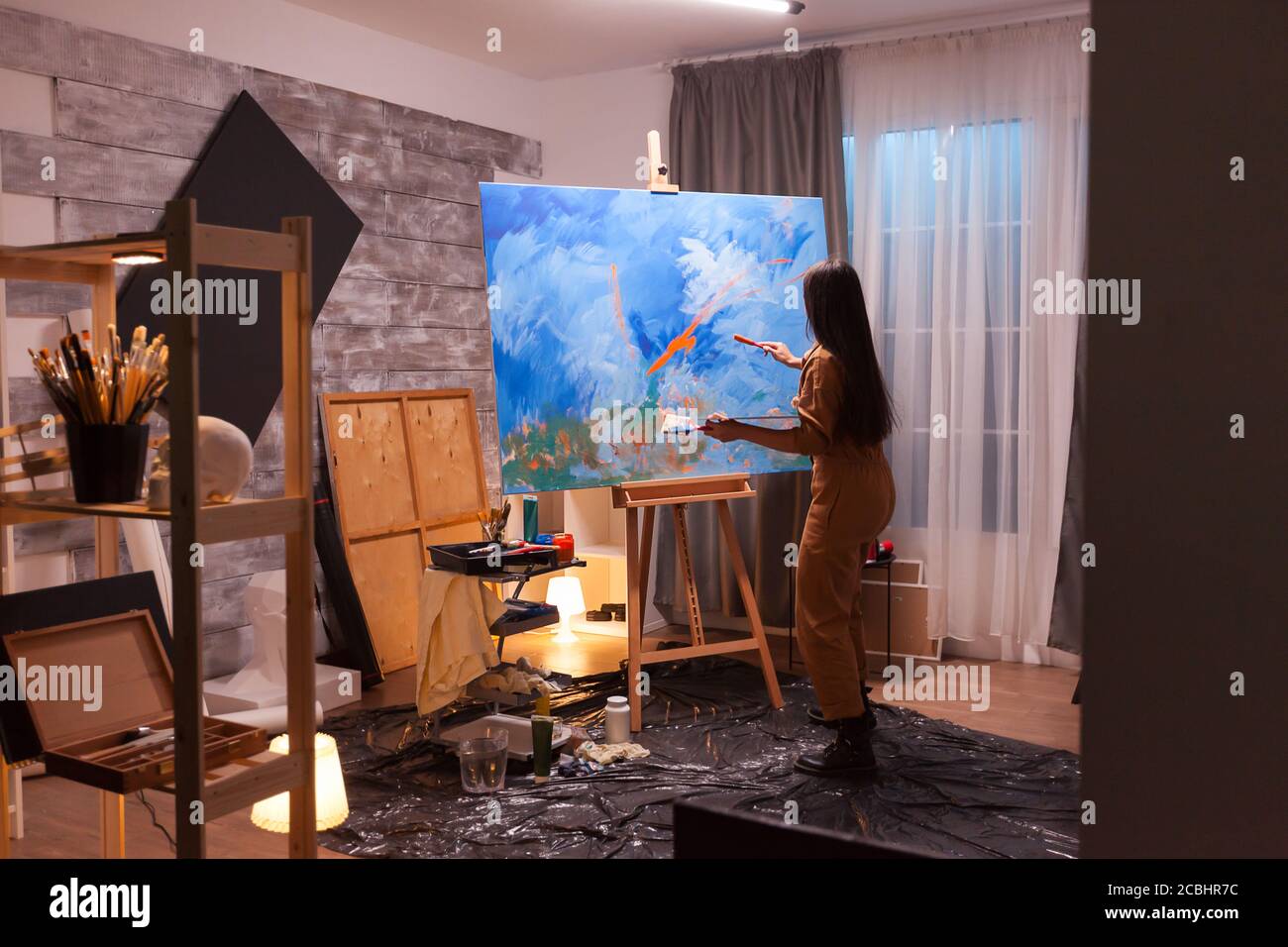 Abstract painter in art studio painting on large canvas with brush ...