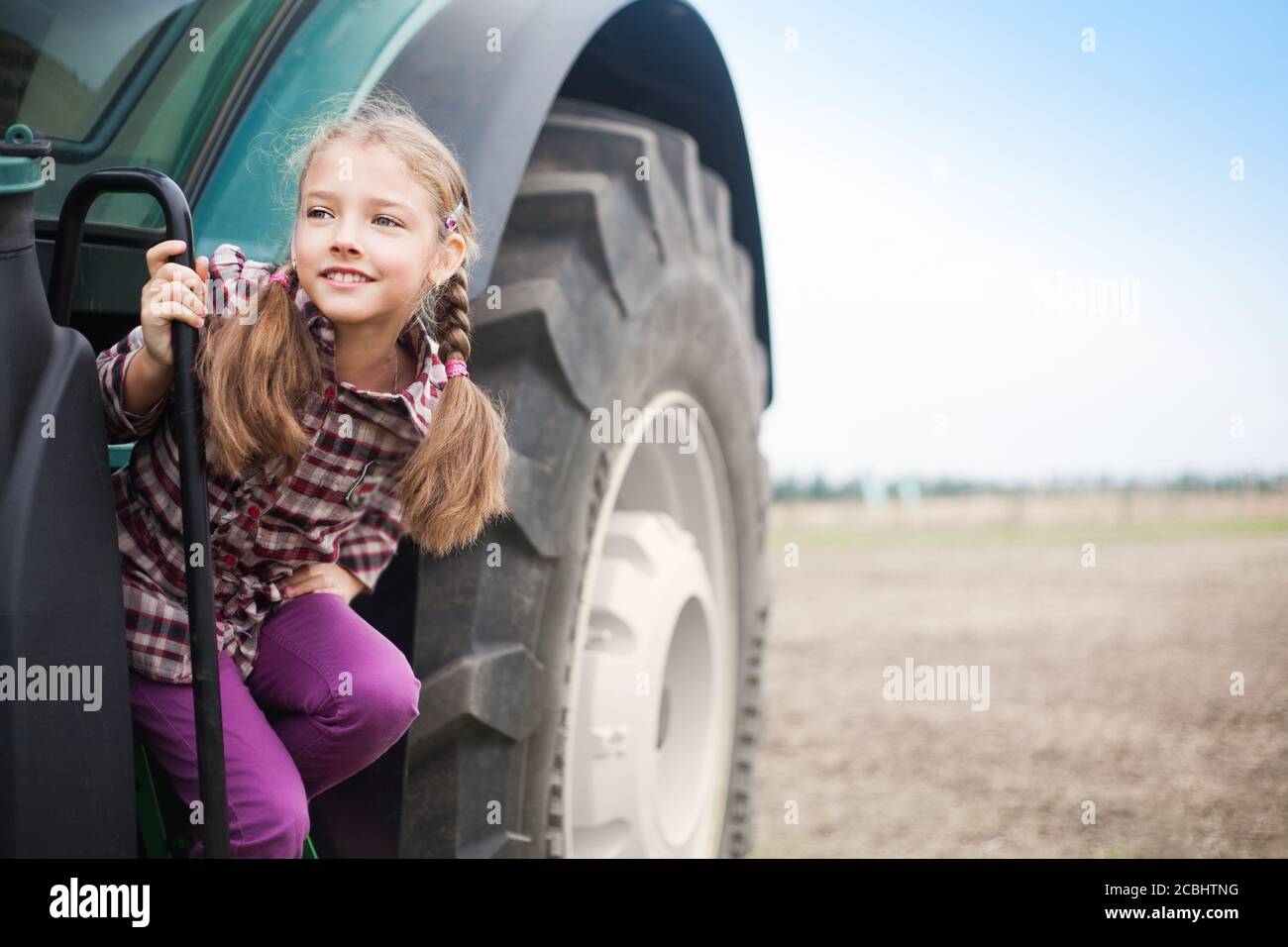 Cute girl near the modern tractor in the field. The concept of field ...