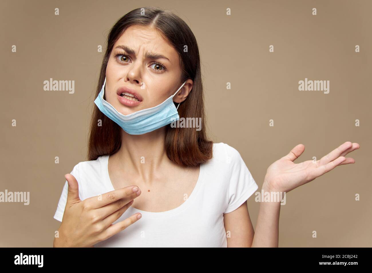 Woman in medical mask shows with hands to the sides on isolated beige ...