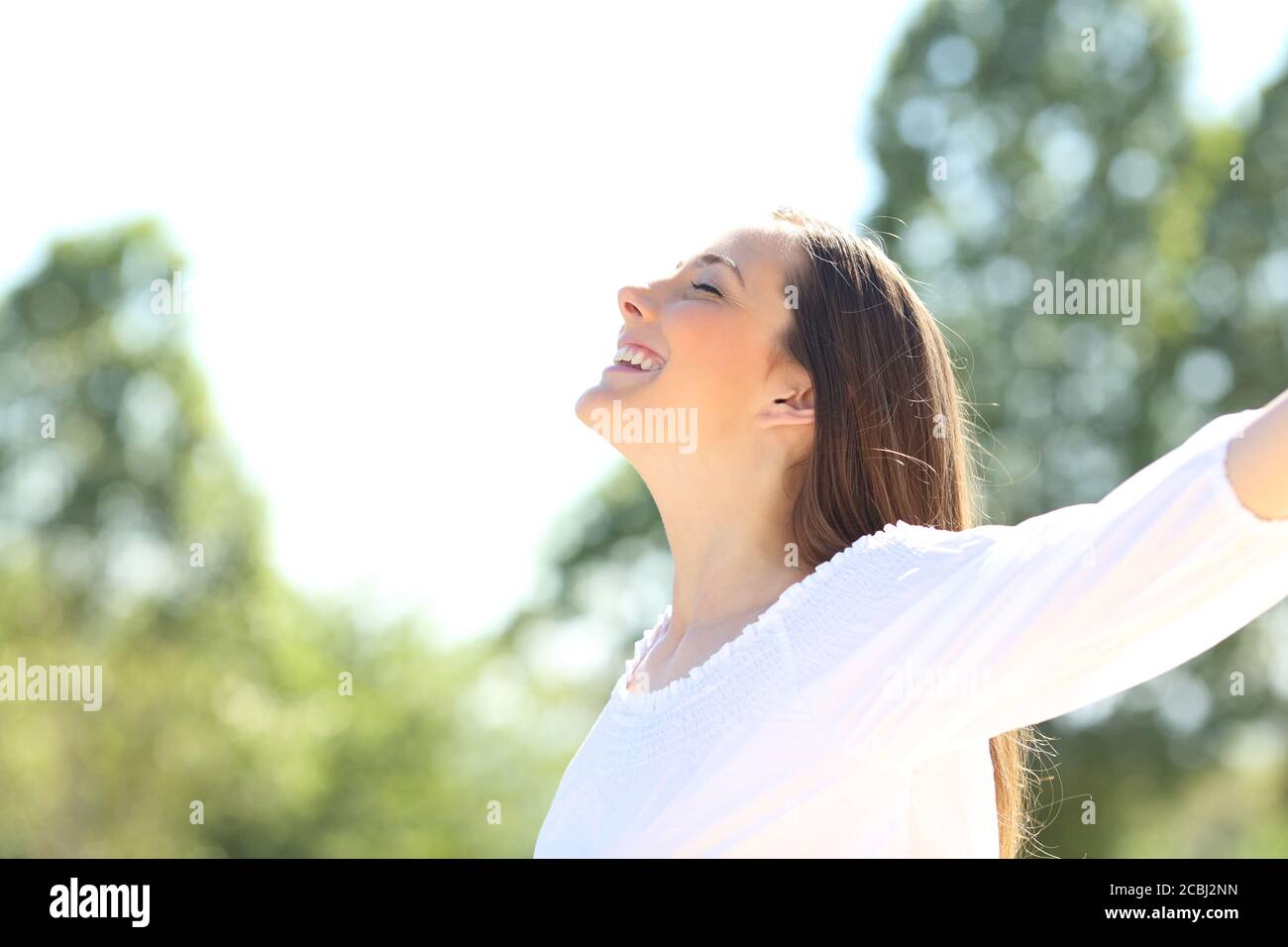 Side view of a happy woman outdoors breathing fresh air spreading arms ...