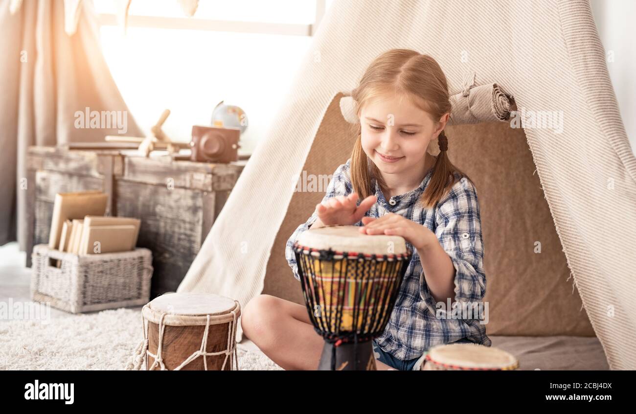 Little drummer girl playing on djembe sitting in front of ethnic tent ...