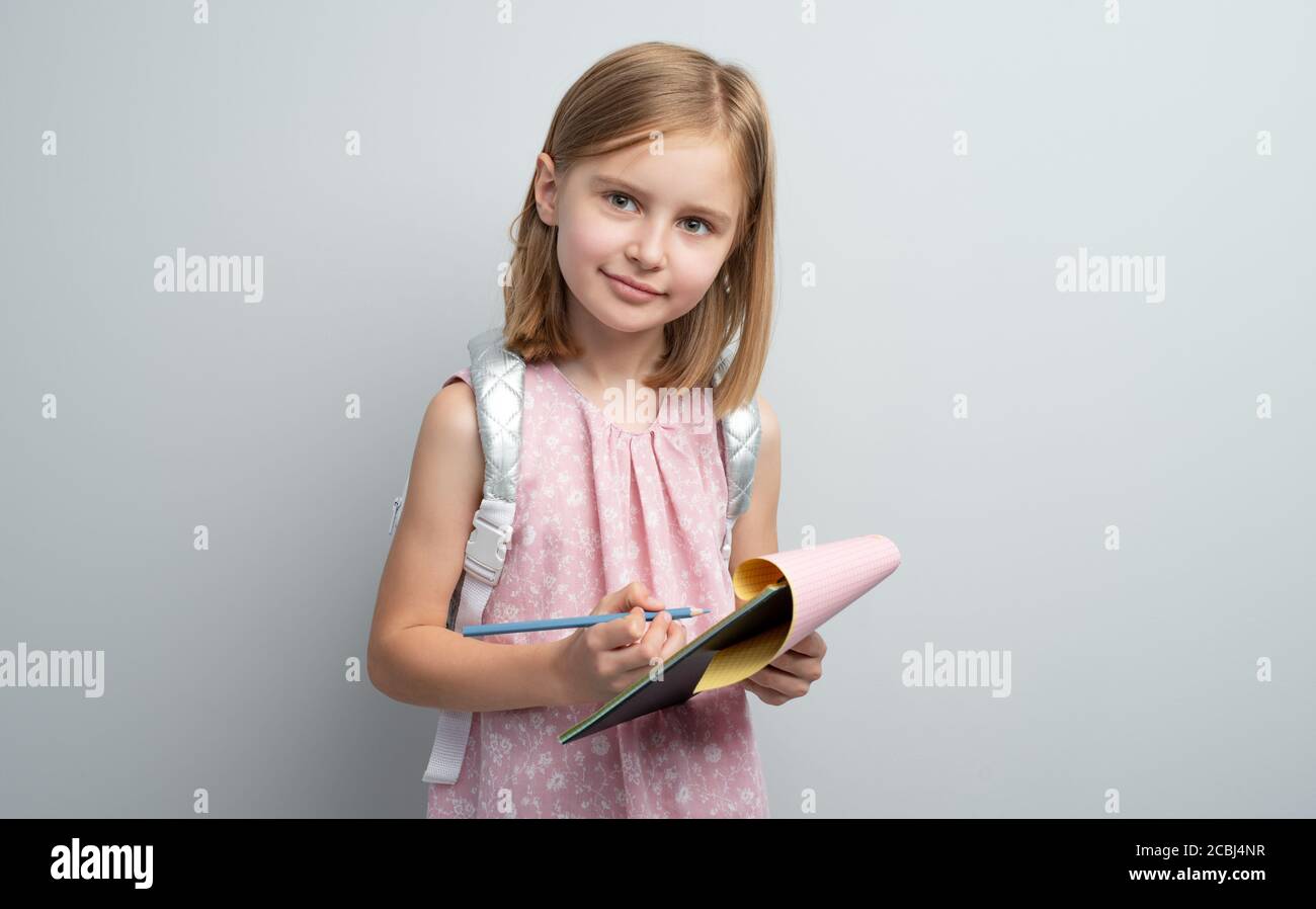 Schoolgirl with pencil taking notes in writing pad on a grey wall ...