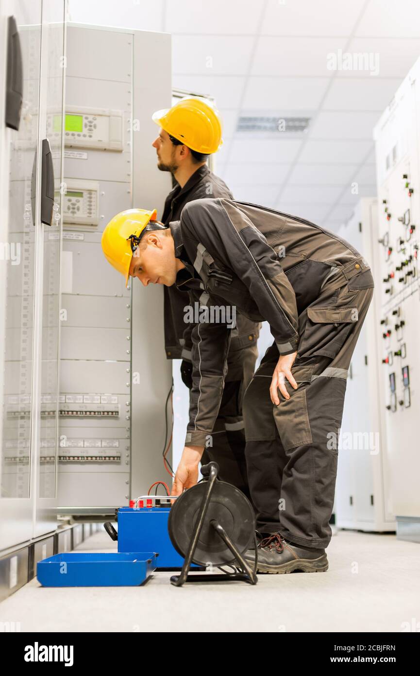 Two field service crew engineers inspect system with relay test set ...