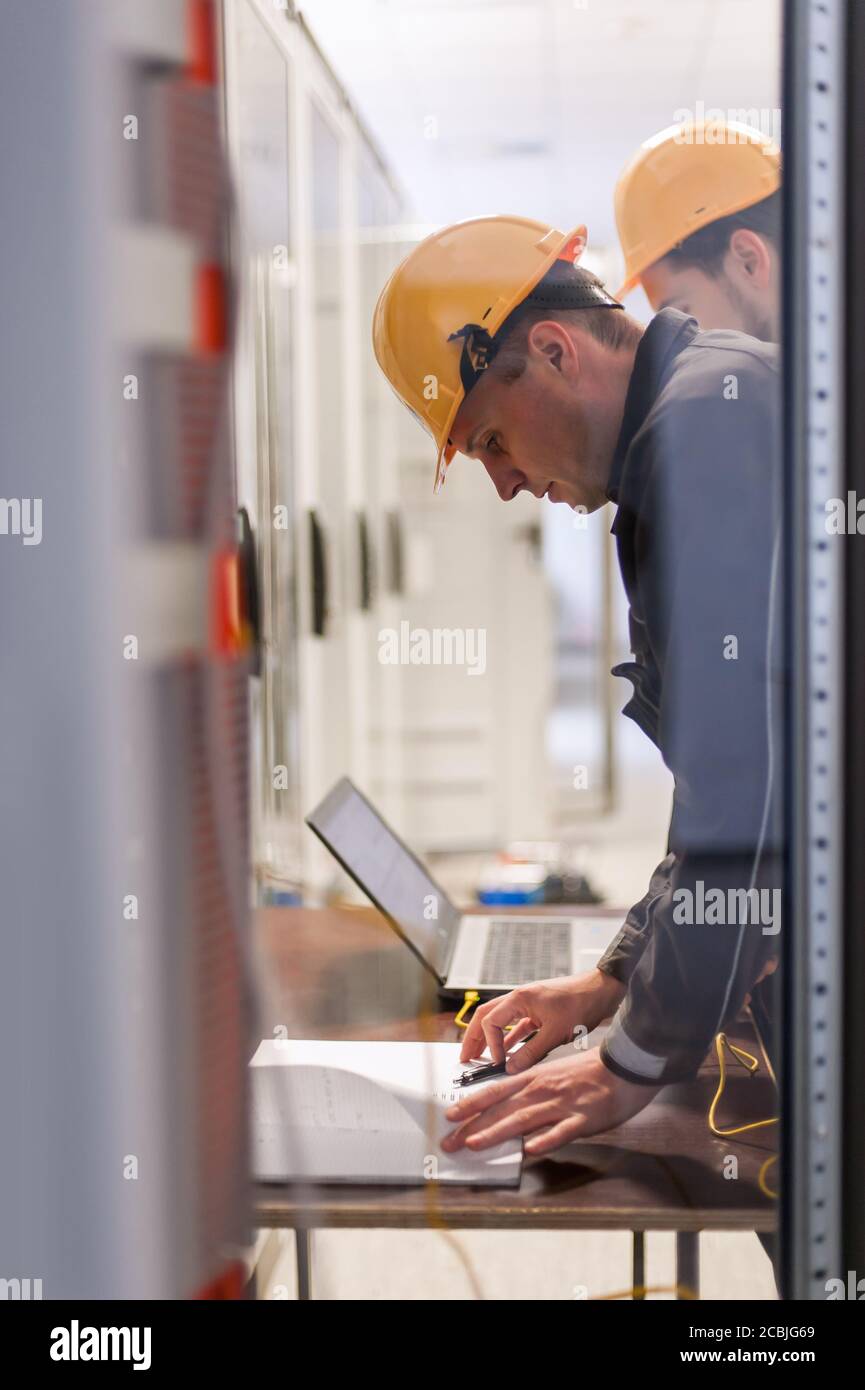 Two maintenance engineers inspect relay protection system with laptop ...