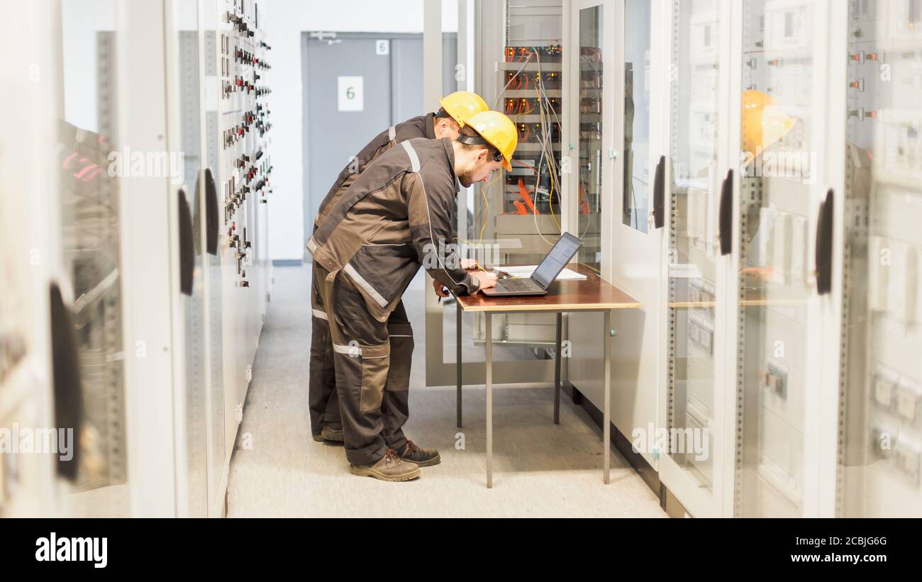 Two maintenance engineers inspect relay protection system with laptop ...