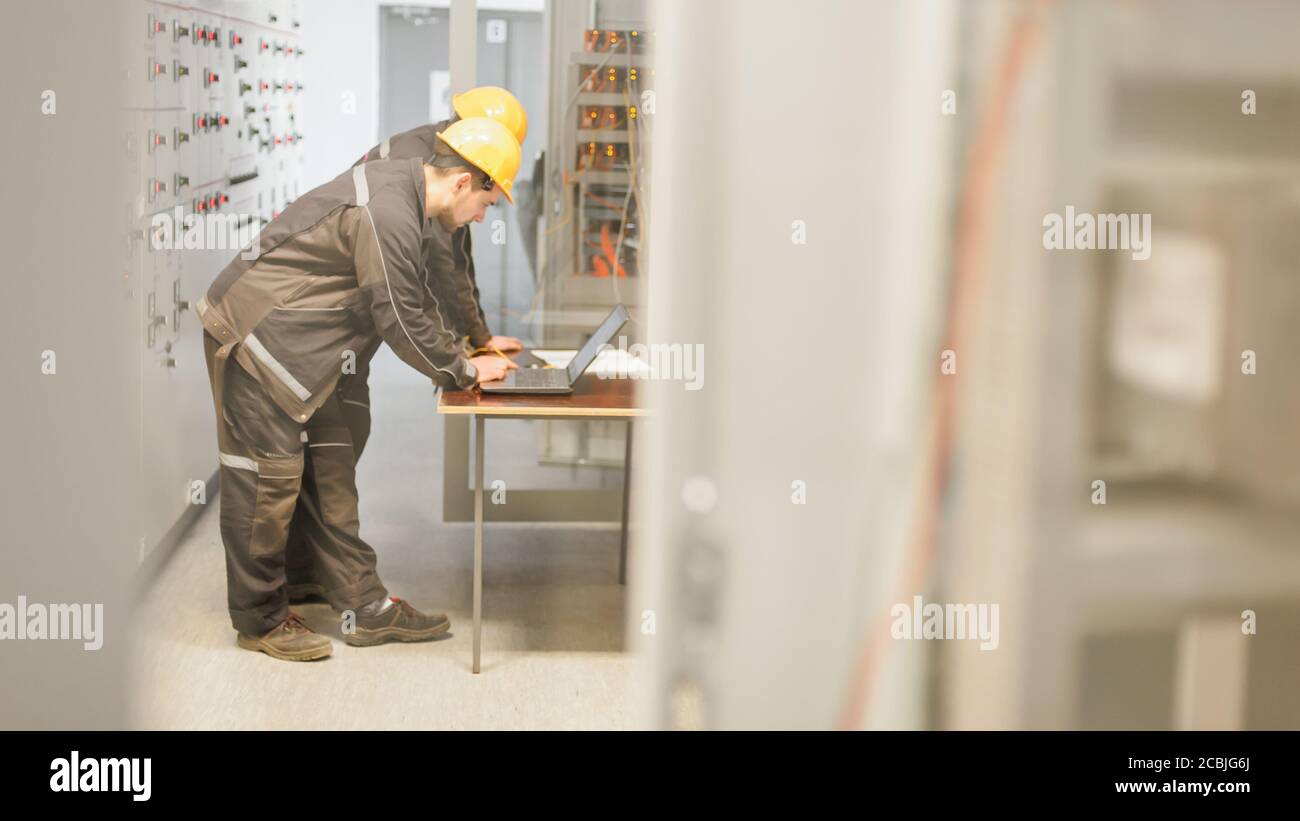 Two maintenance engineers inspect relay protection system with laptop ...