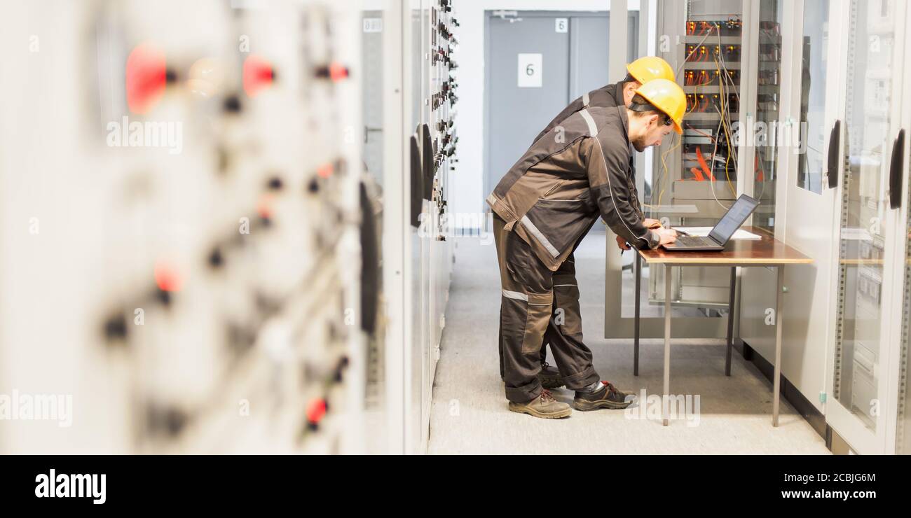 Two maintenance engineers inspect relay protection system with laptop ...