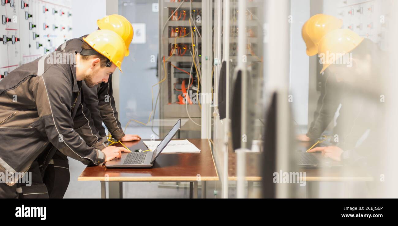 Two maintenance engineers inspect relay protection system with laptop ...