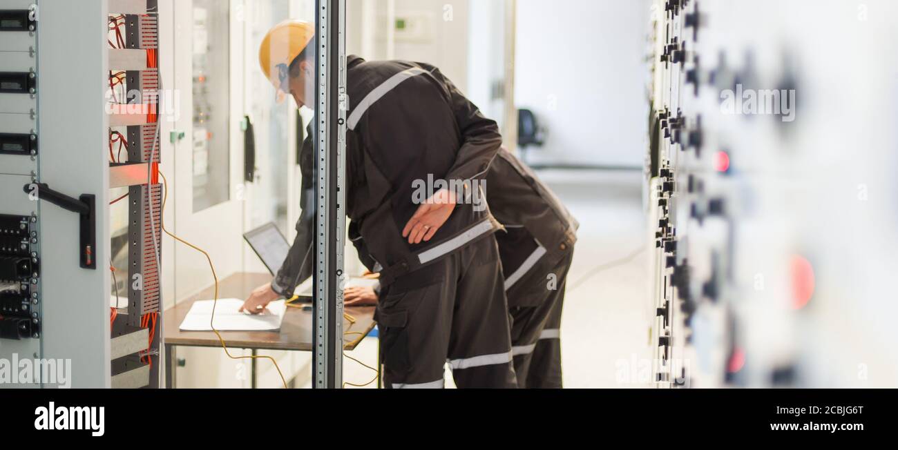 Two maintenance engineers inspect relay protection system with laptop ...