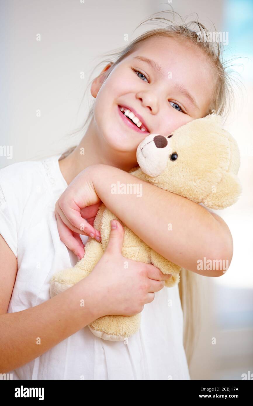 Happy girl snuggles up to her cuddly toy at home Stock Photo - Alamy