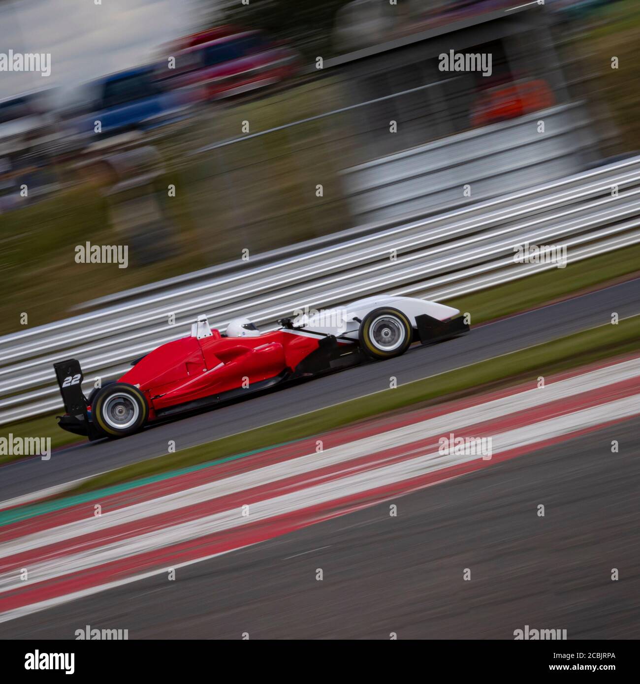 A panning shot of a red and white racing car as it circuits a track ...
