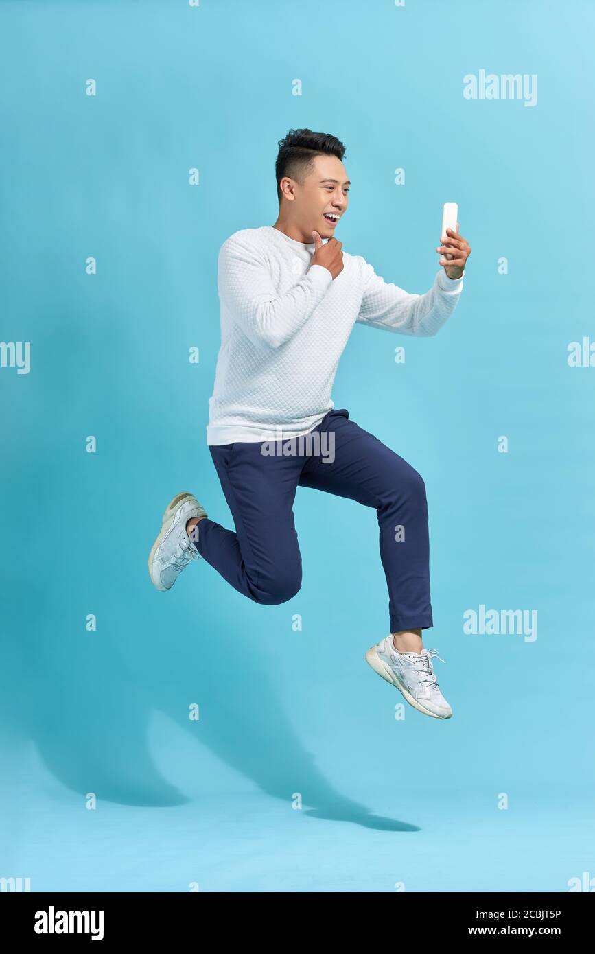 Full length of handsome young man taking phone while jumping against ...