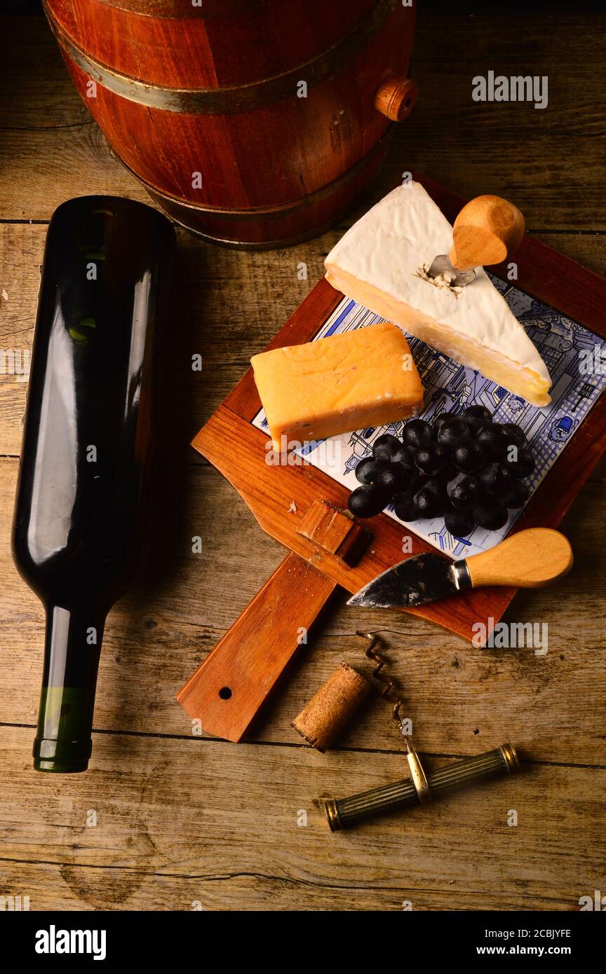 Bottle and glass of wine with an assorted table of cheese and a barrel ...