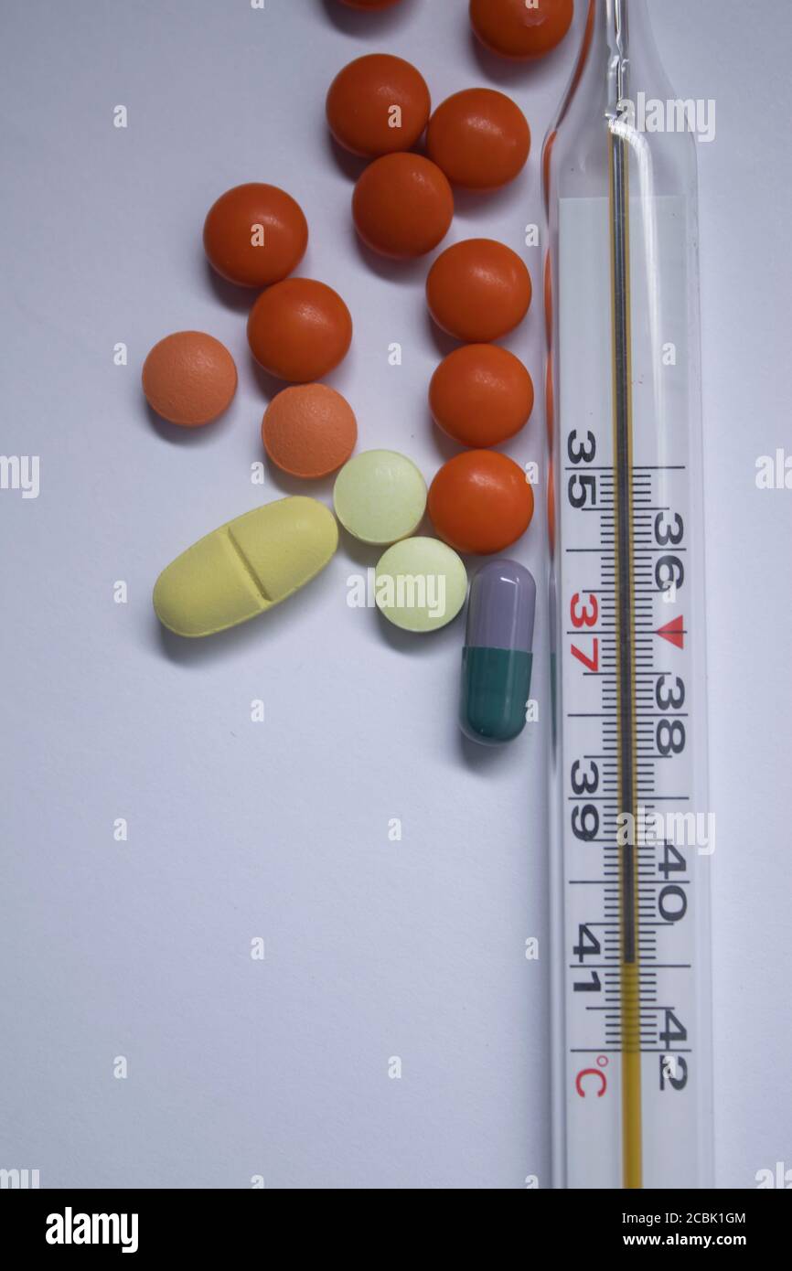 mercury thermometer with a bunch of pills on a white background ...