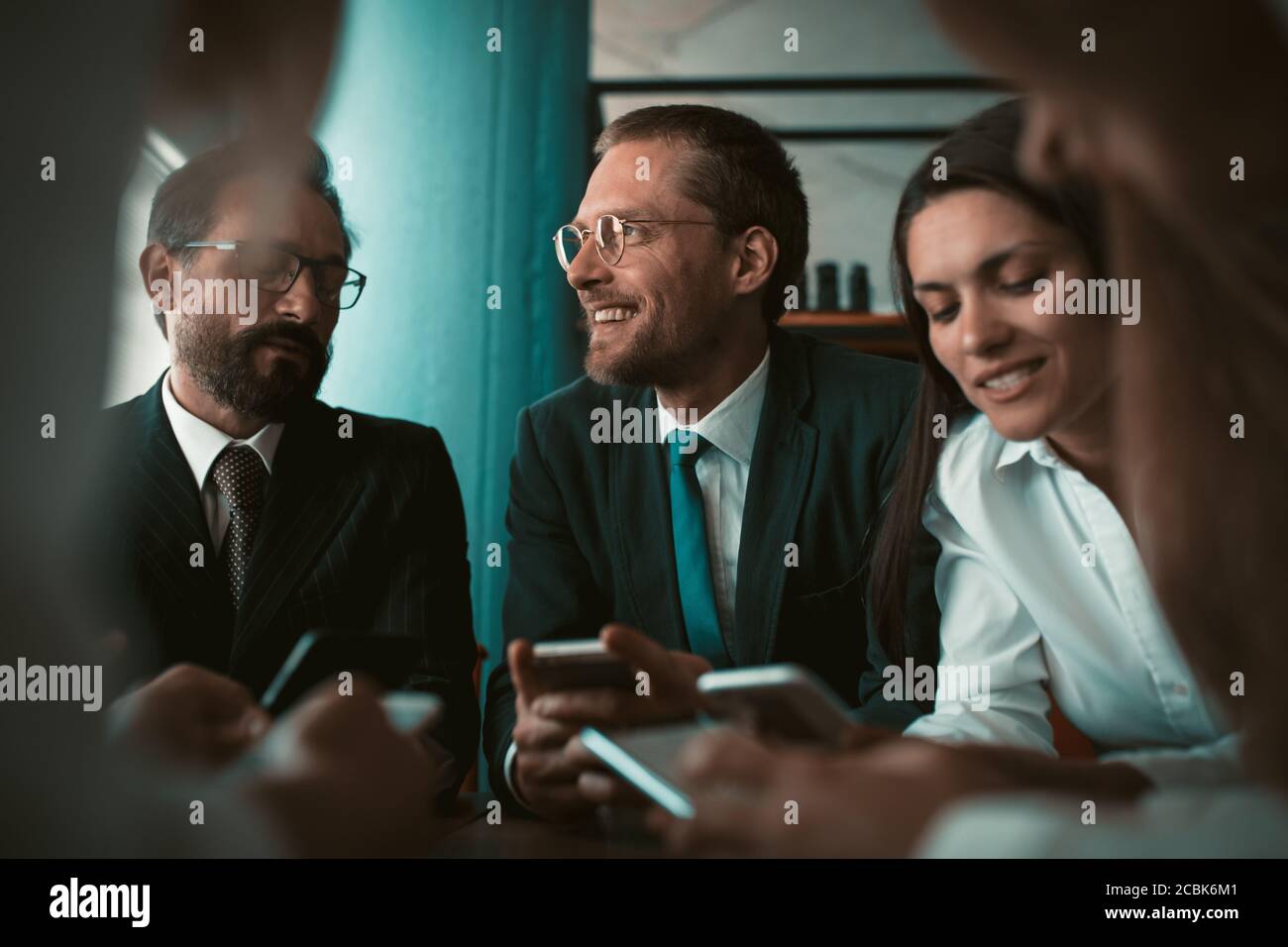 Group of smiling businesspeople using phones while communicating in ...