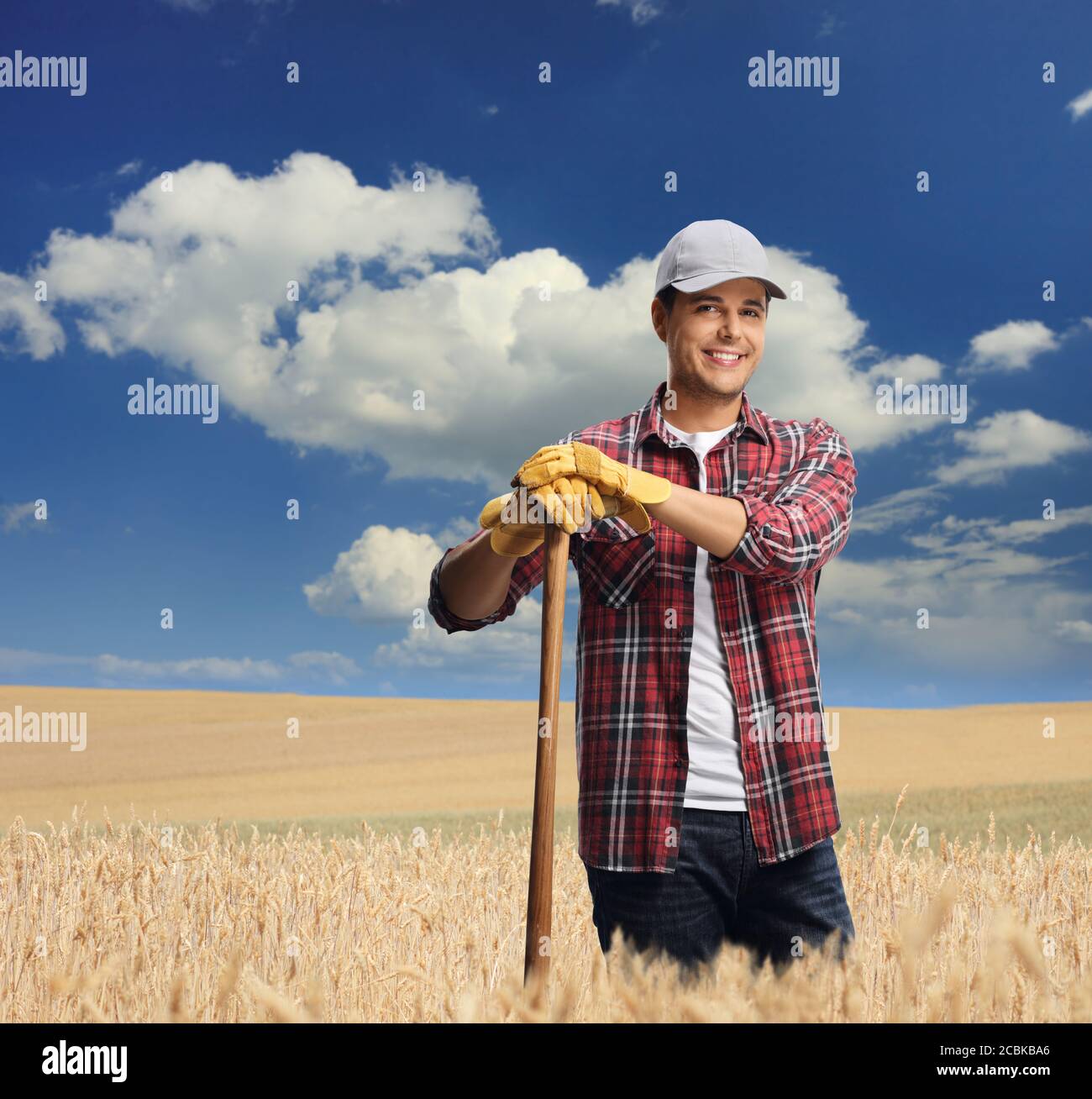 Male farmer with a wooden tool standing in a wheat field and smiling at ...