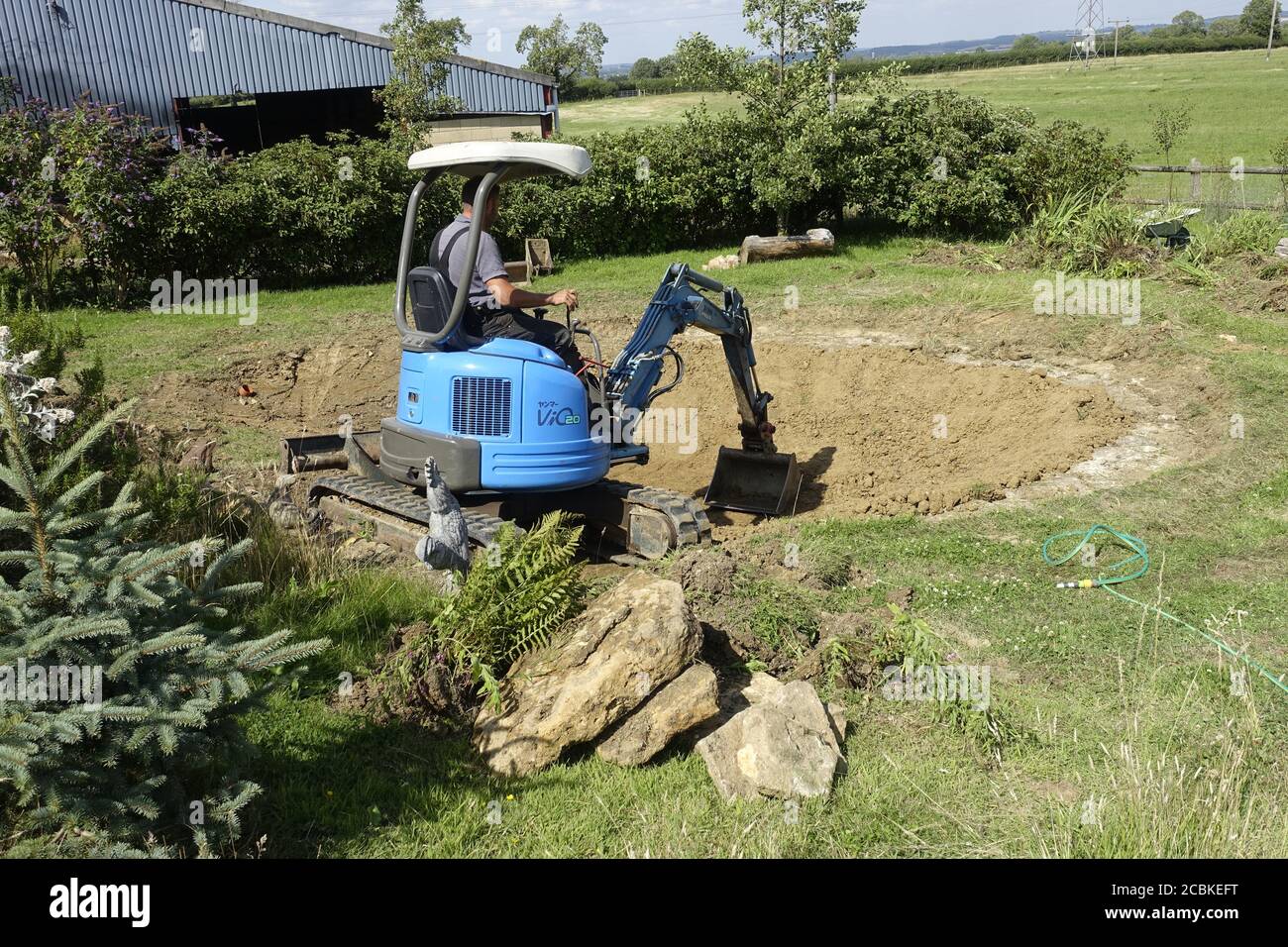 Workman in excavator removing soil from large silted up pond in ...