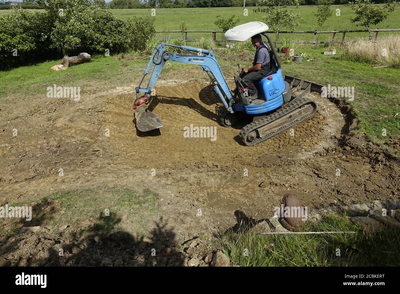 Workman in excavator removing soil from large silted up pond in ...