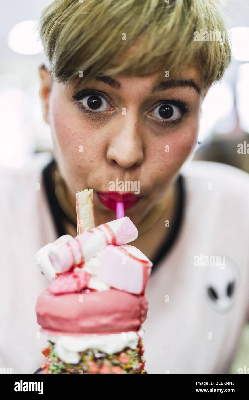 A vertical shot of a young female drinking a pink milkshake with ...