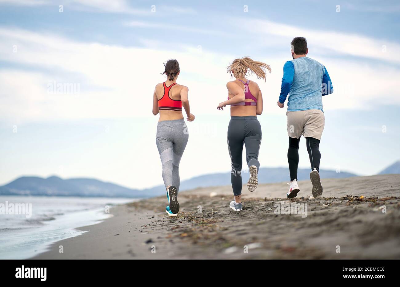 Group of three people jogging together on the beach Stock Photo - Alamy
